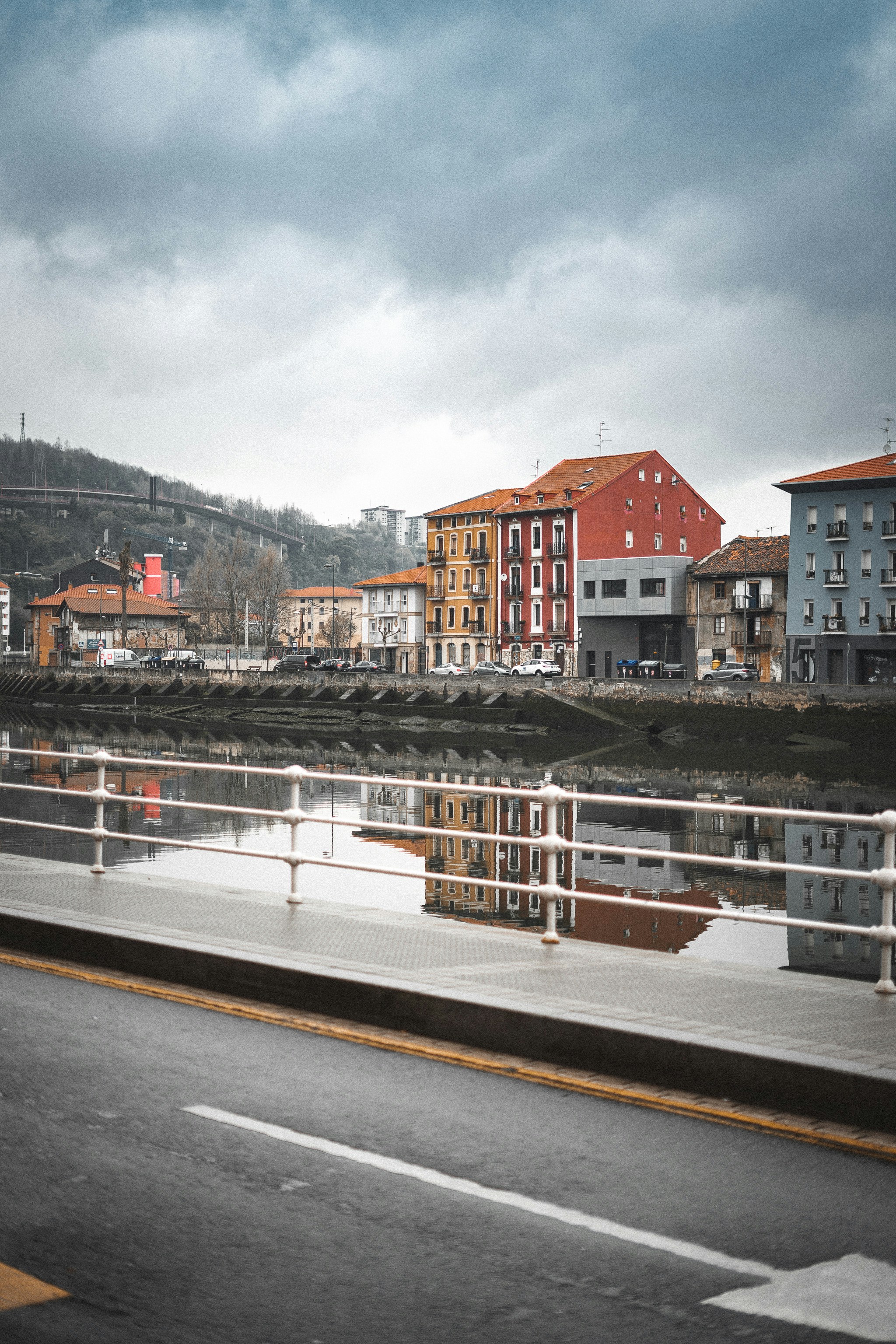Vibrant buildings reflecting in a calm river, framed by a cloudy sky. The scene captures the essence of urban life along the water's edge.