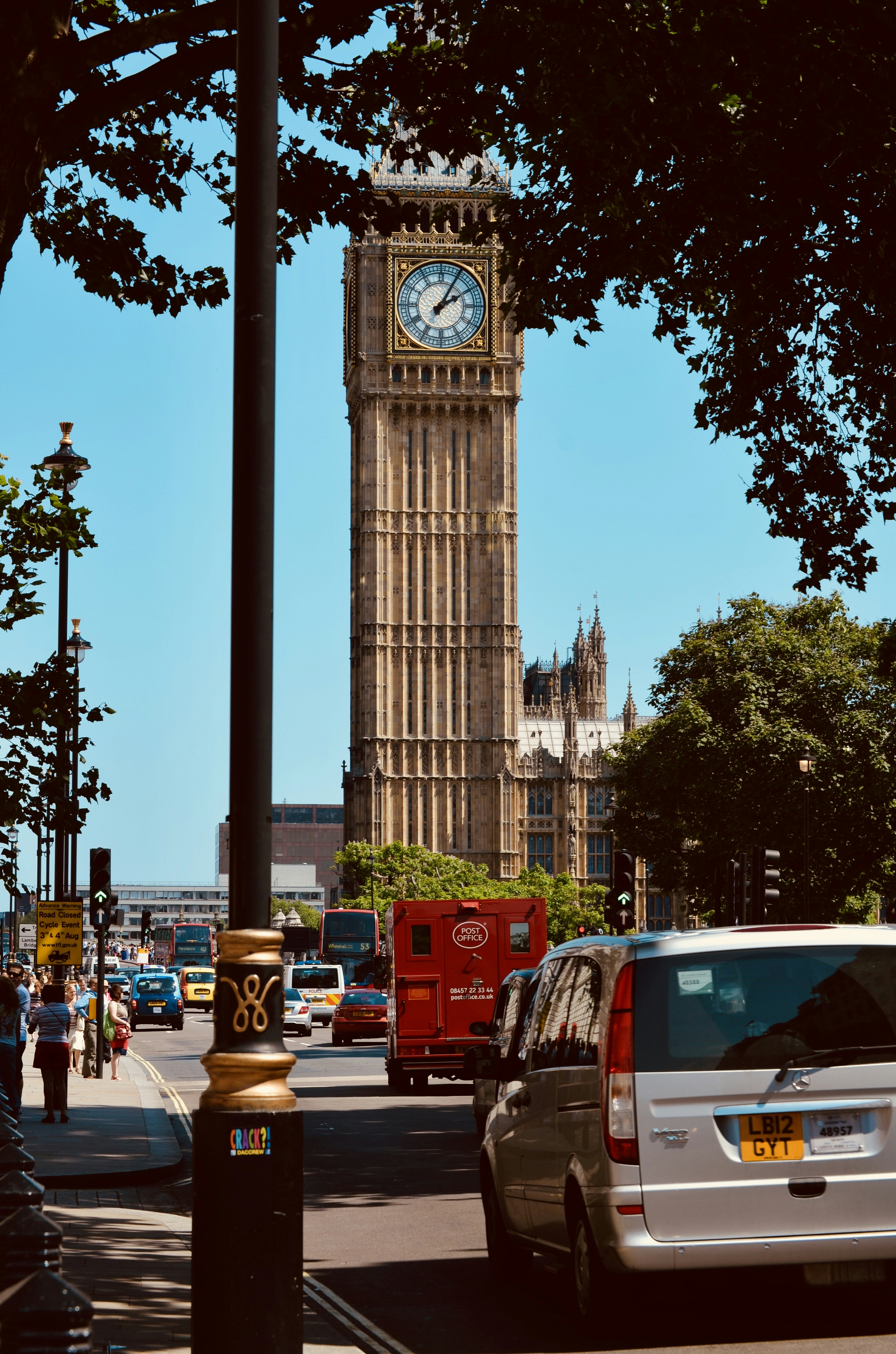 Big Ben towering over busy London street, framed by lush trees and urban activity.