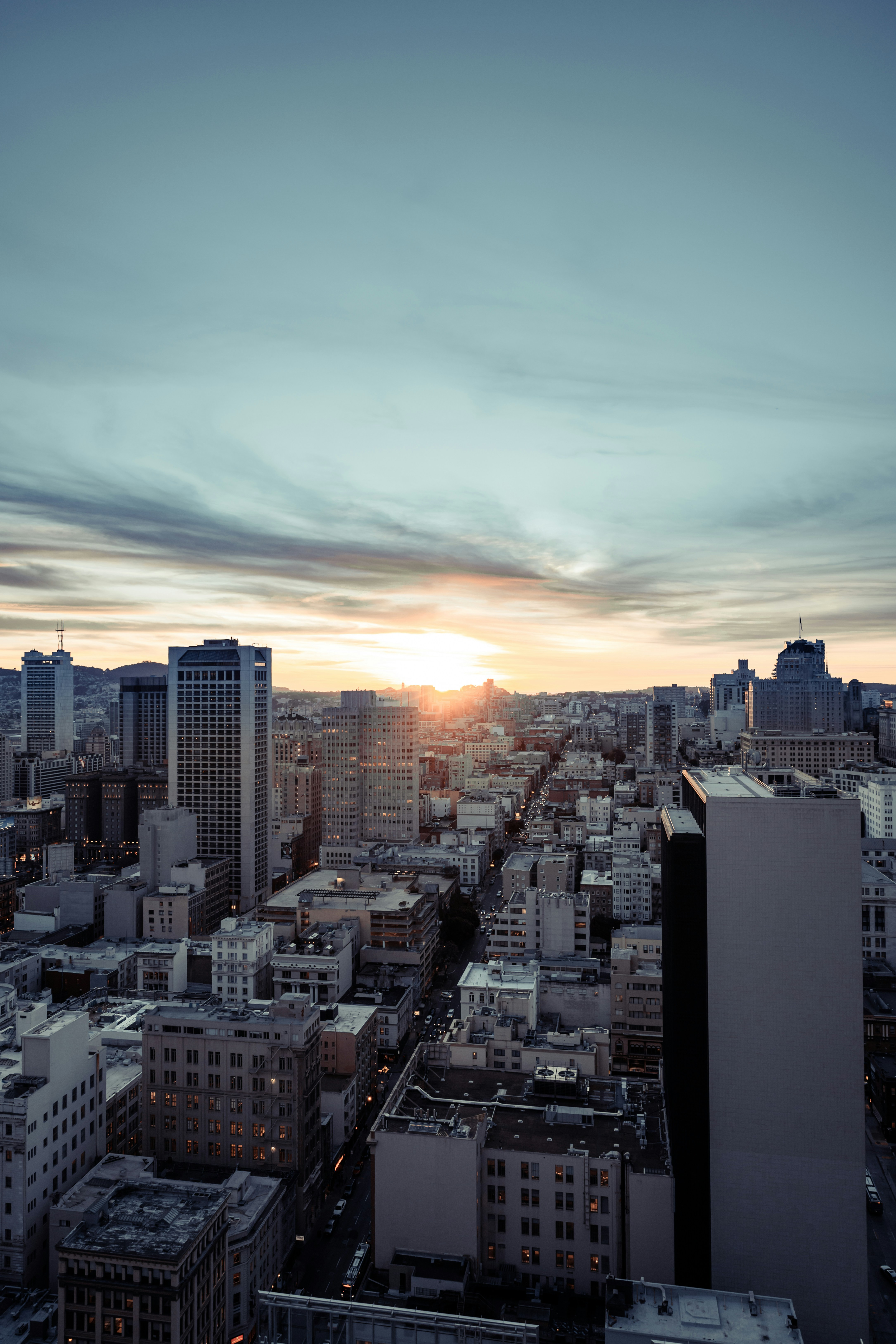 City skyline at sunset, showcasing a blend of modern architecture and warm light. The horizon glows as day transitions to night.