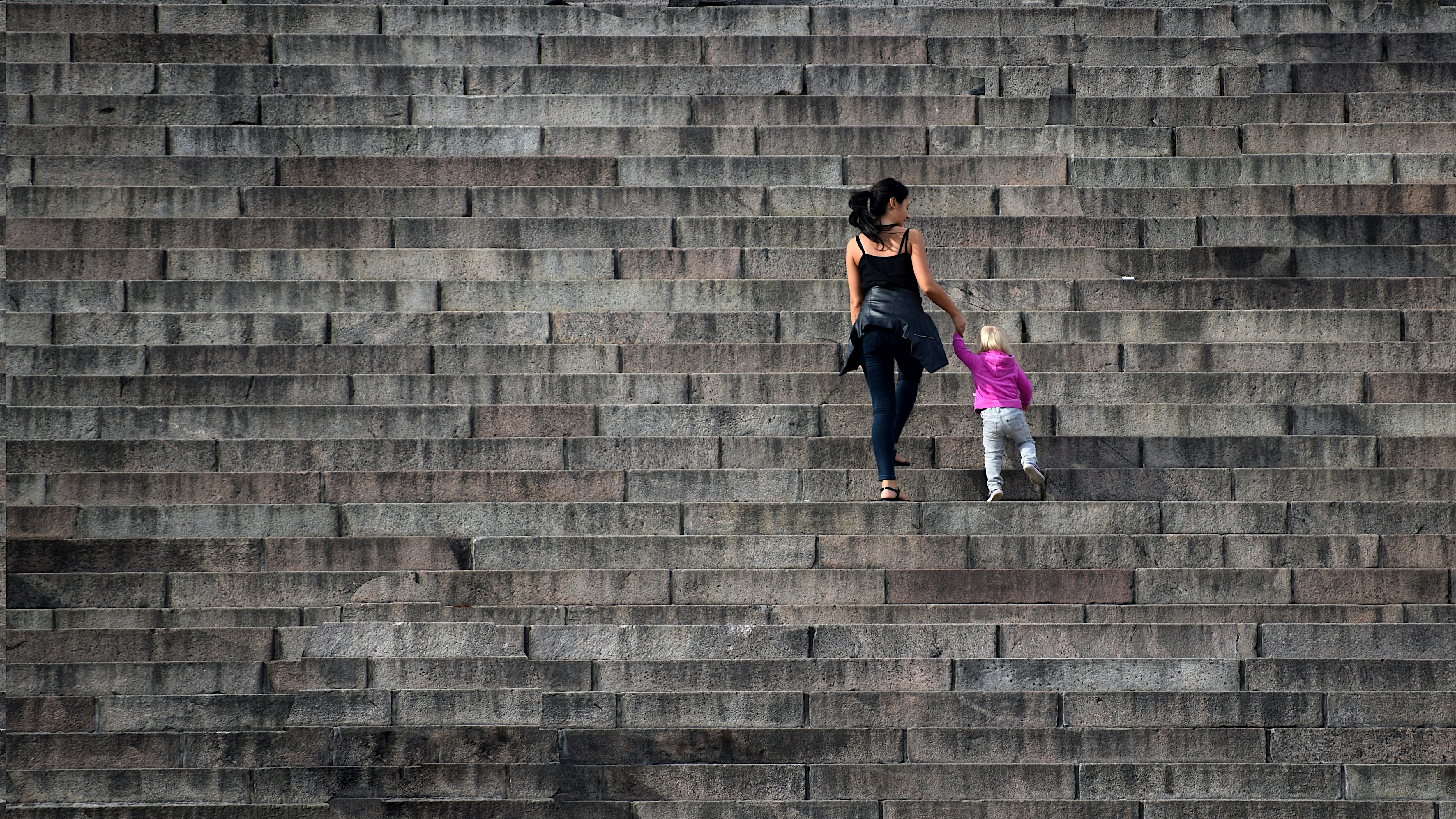 Woman and child descending expansive stone steps, holding hands.