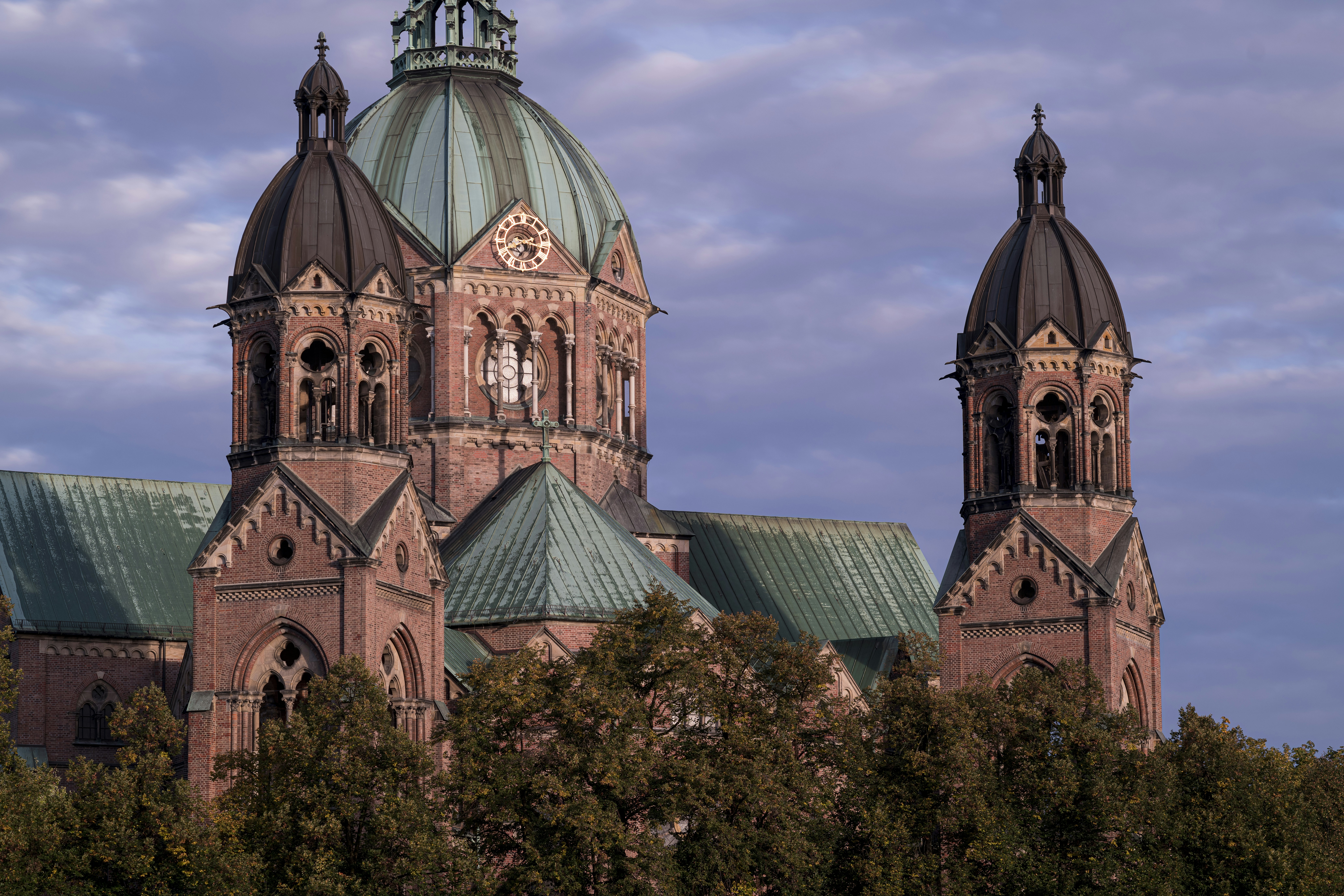 Historic cathedral featuring intricate towers and a distinctive green copper roof, framed by lush trees.