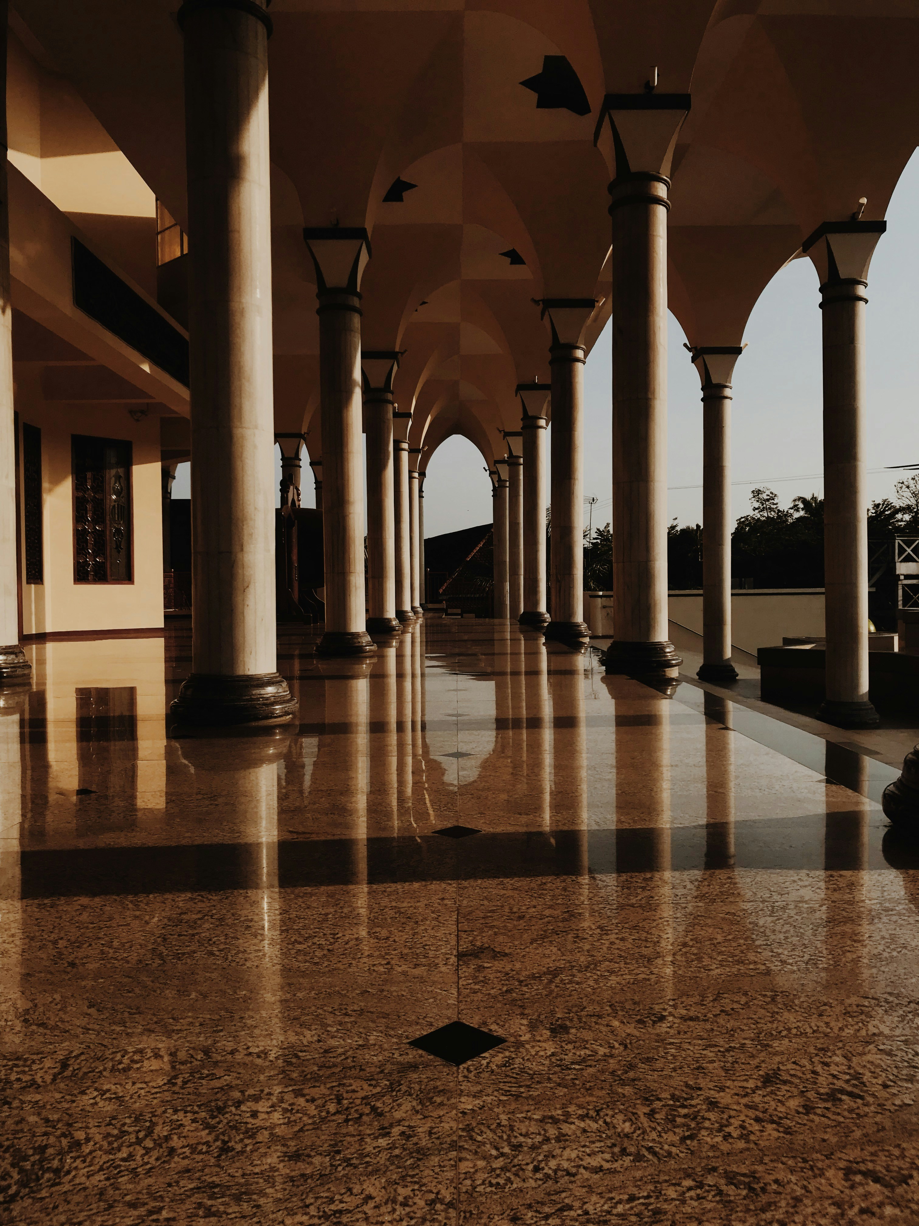 Sunlight casts long shadows through the columns of a mosque, reflecting on the polished floor.