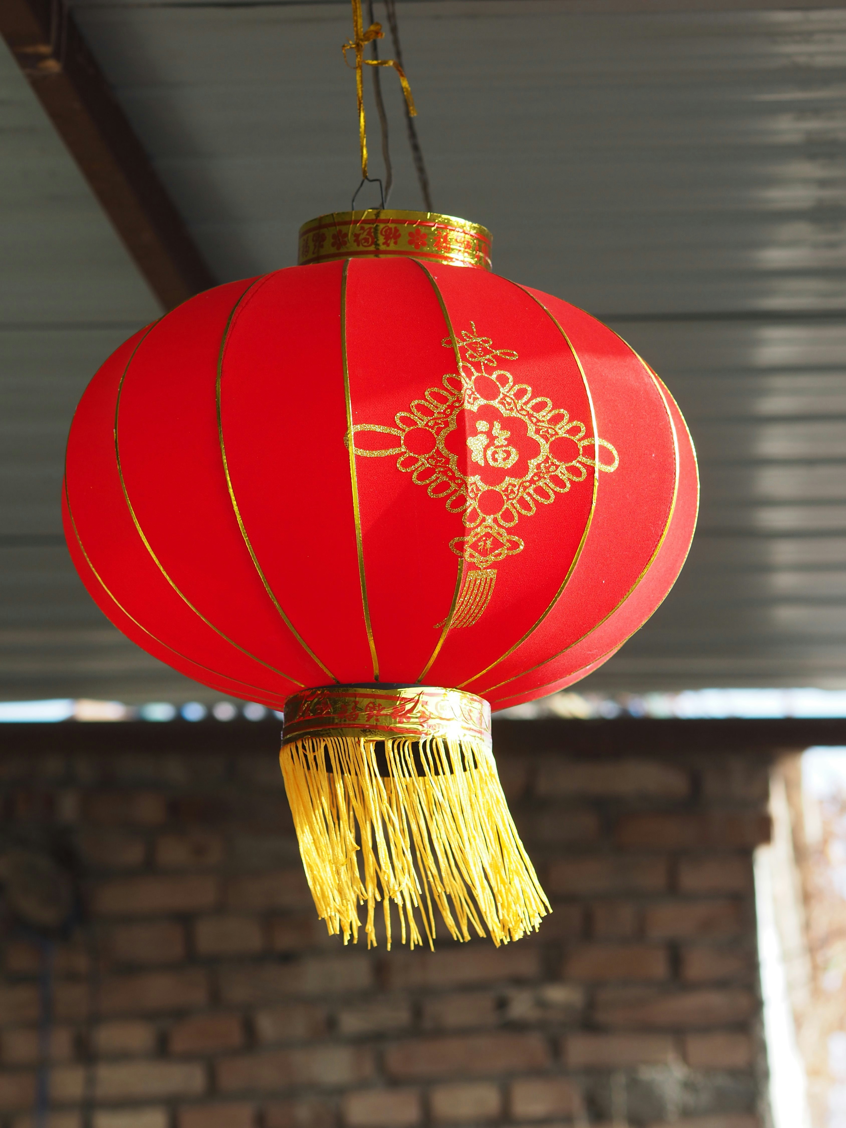 Crimson Lantern in Quiet Light: Gold Tassels Against Brick Backdrop