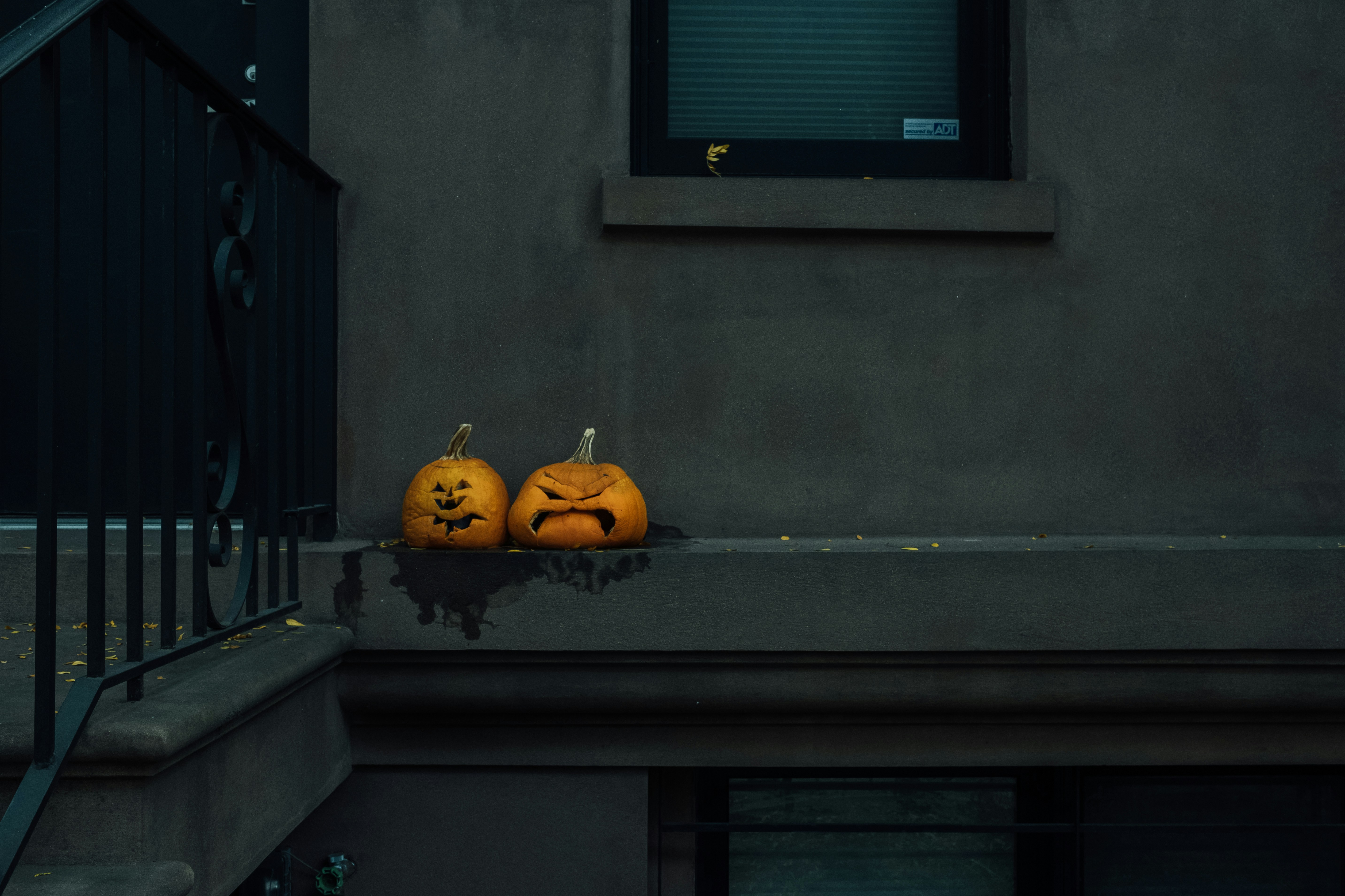 Two carved pumpkins with contrasting expressions sit on a ledge against a muted wall, embodying the spirit of Halloween.