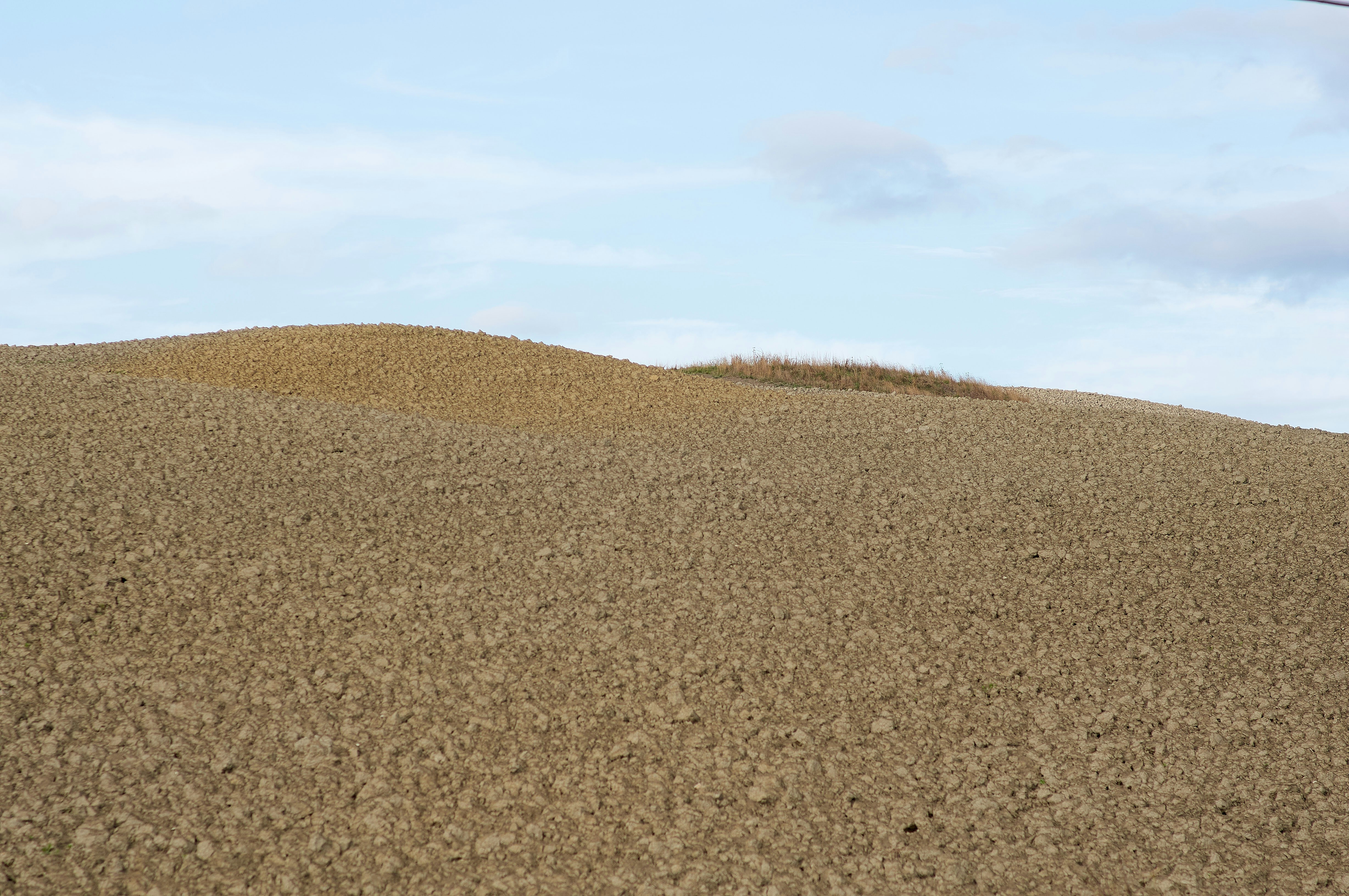 Gentle rolling hills of dry earth under a soft blue sky, highlighting the textures of the terrain. The scene evokes a sense of calm and natural beauty.