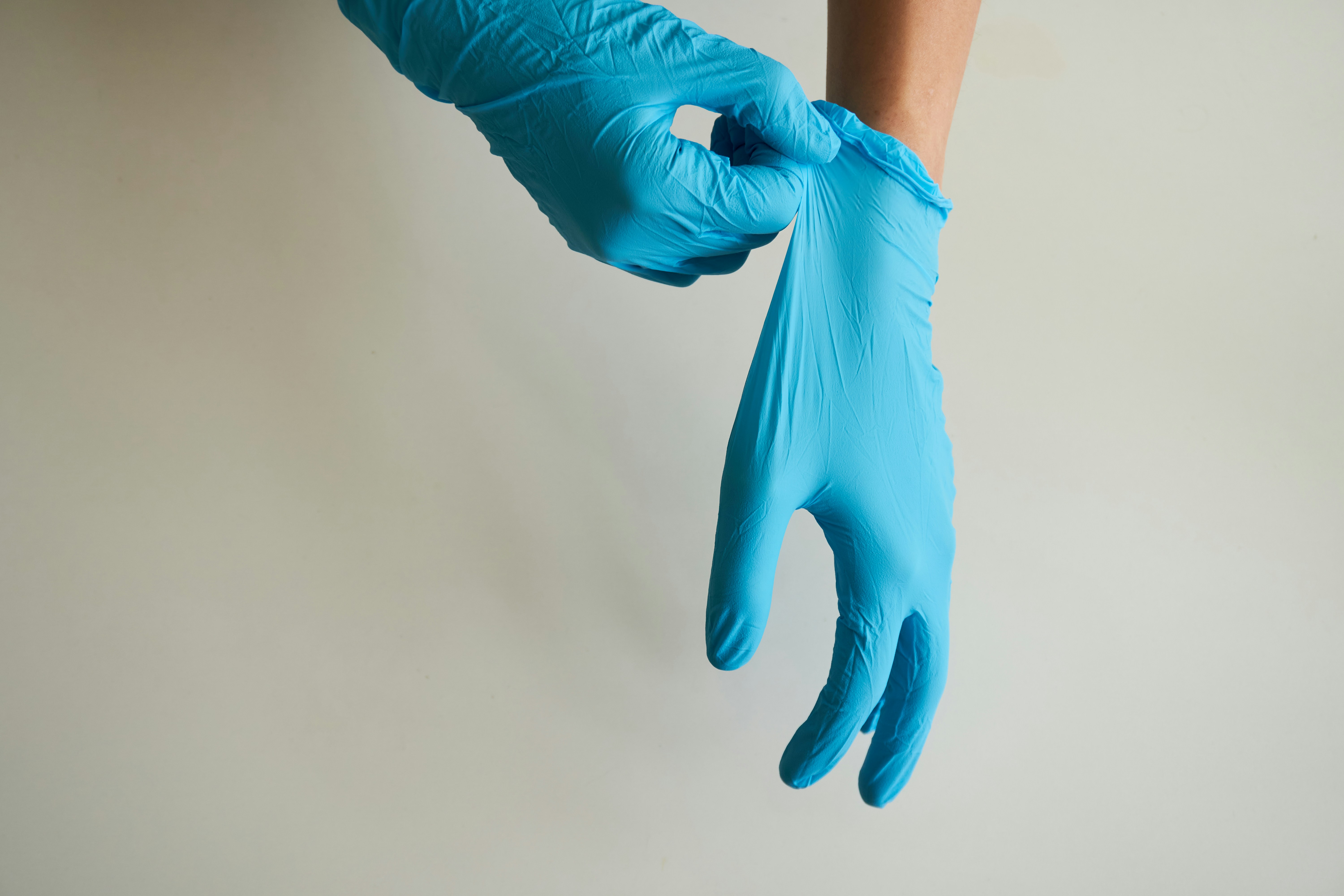 Hands donning blue medical gloves against a neutral background, emphasizing preparation for a sterile procedure.