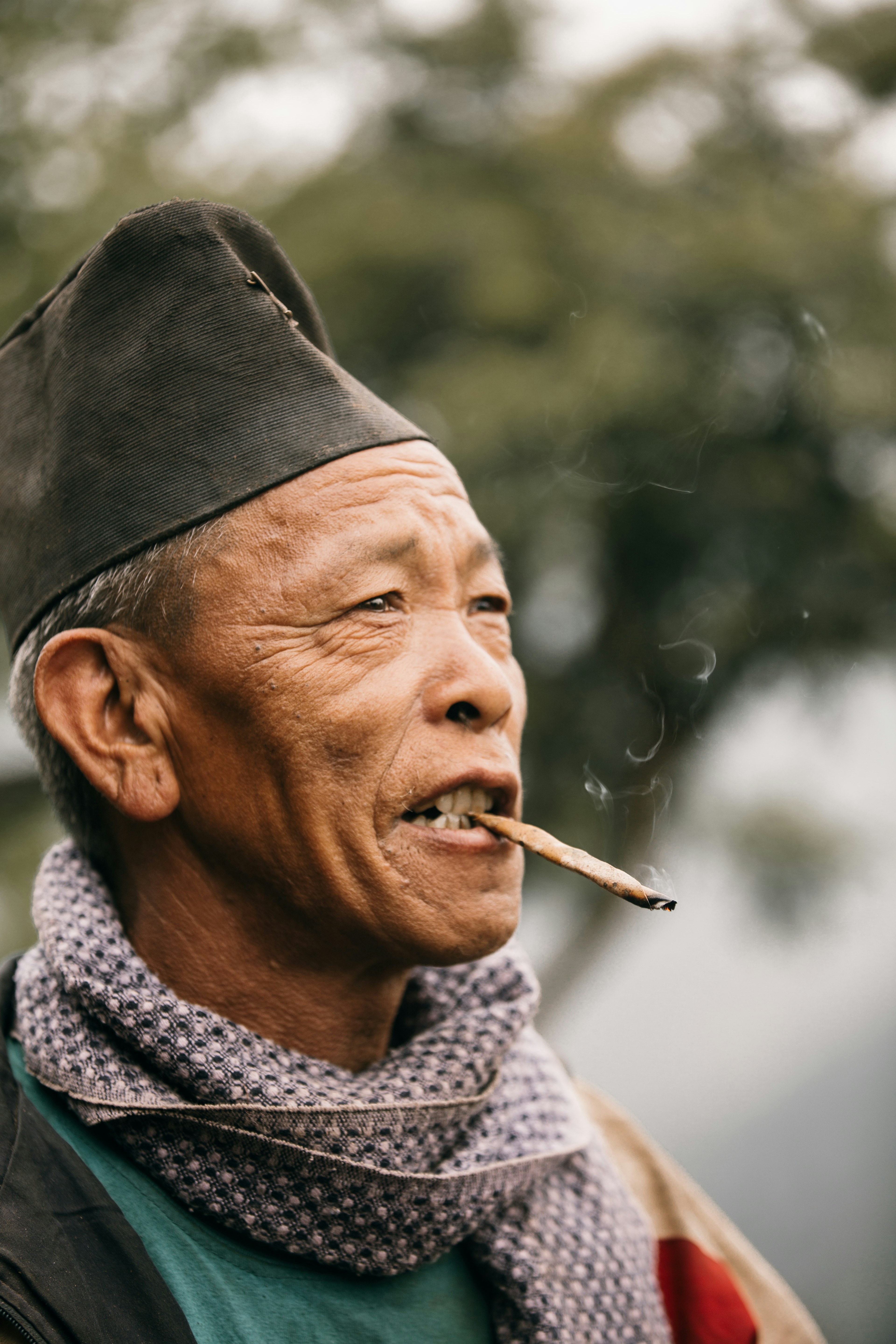 Elderly man with a traditional hat and scarf, smoking a stick, exuding wisdom and cultural heritage.