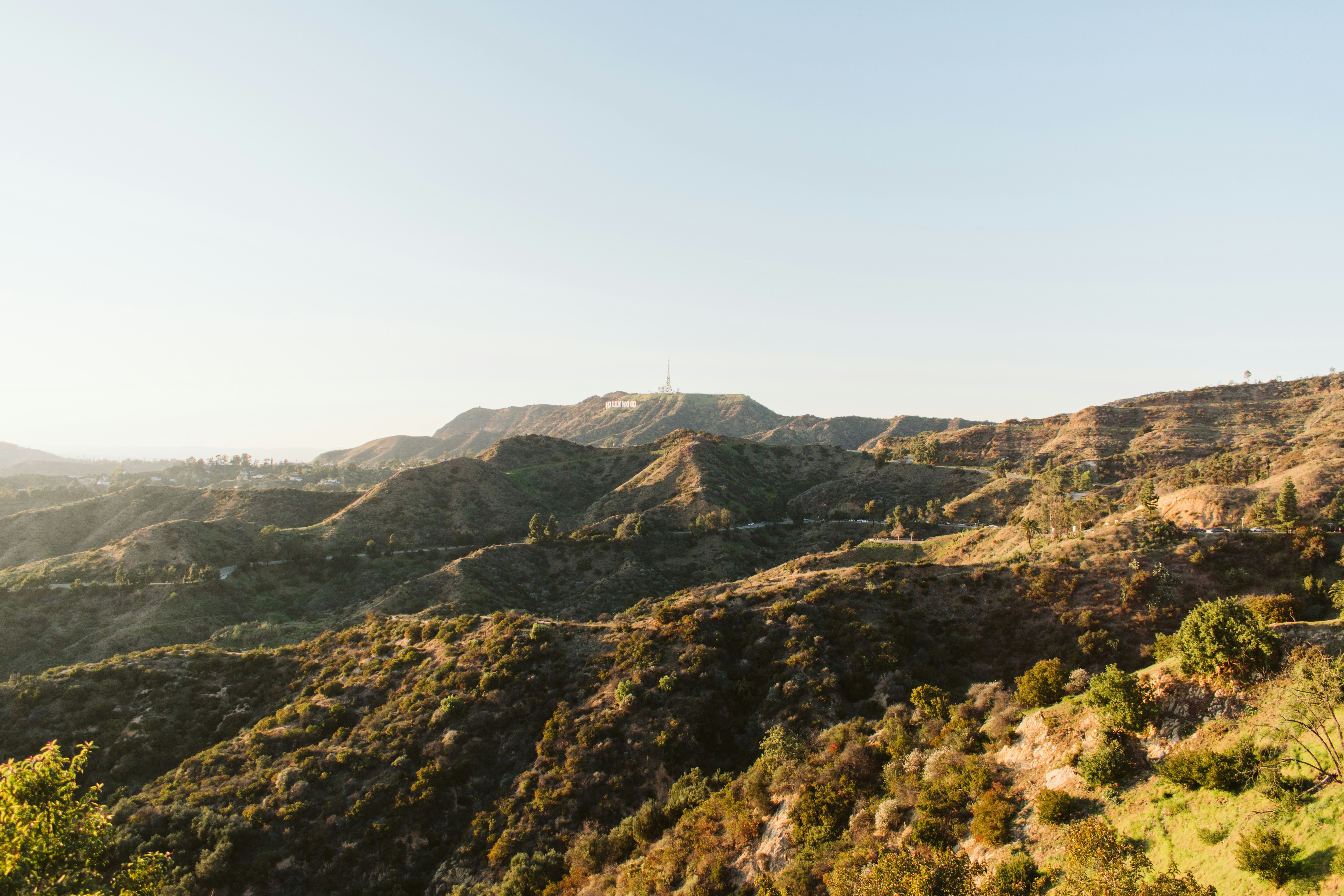 Sunlit hills stretch under a clear blue sky, creating a serene landscape with lush greenery and gentle slopes.