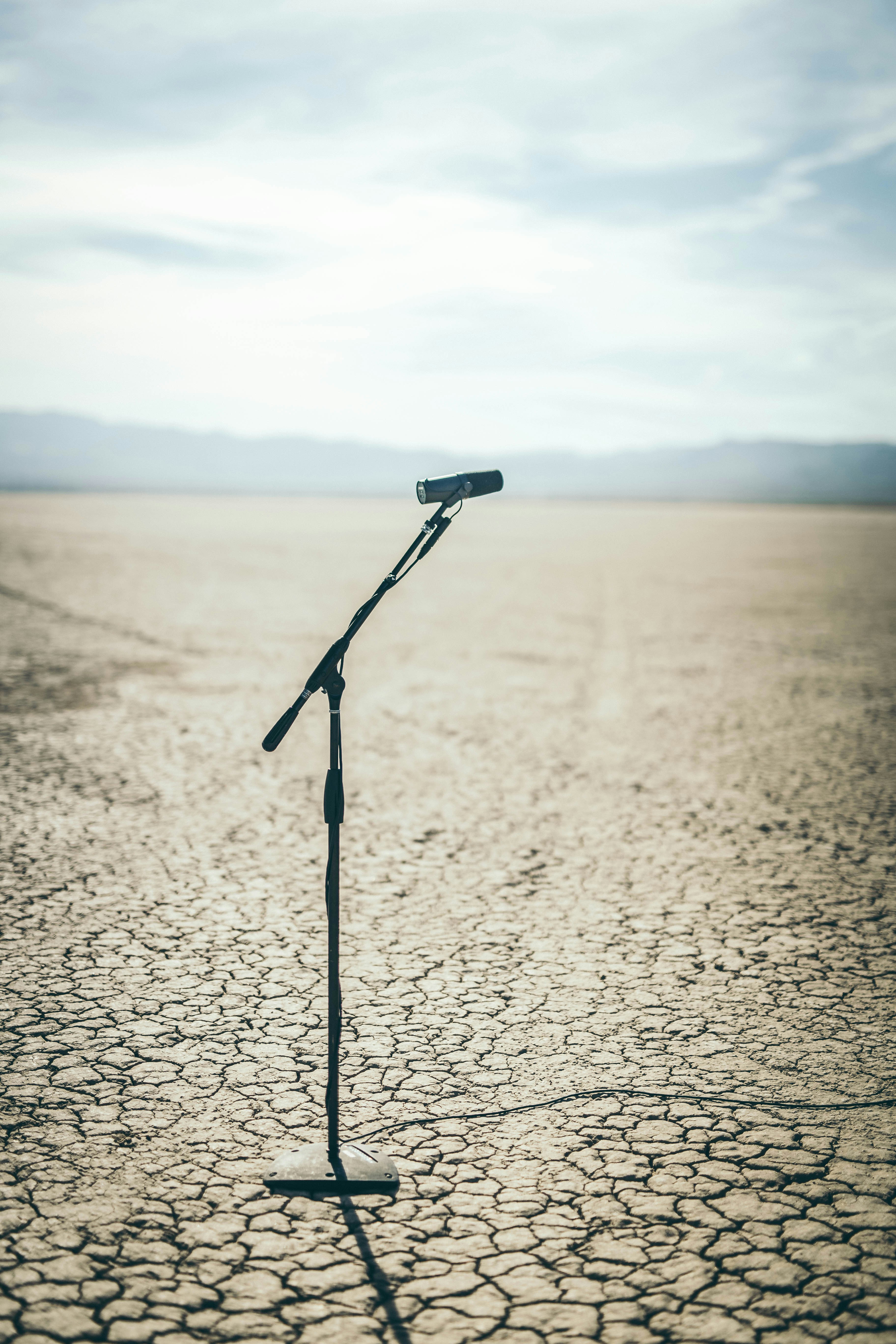 A lone microphone stands on cracked earth, surrounded by an expansive desert landscape under a vast sky. The scene evokes a sense of isolation and potential.