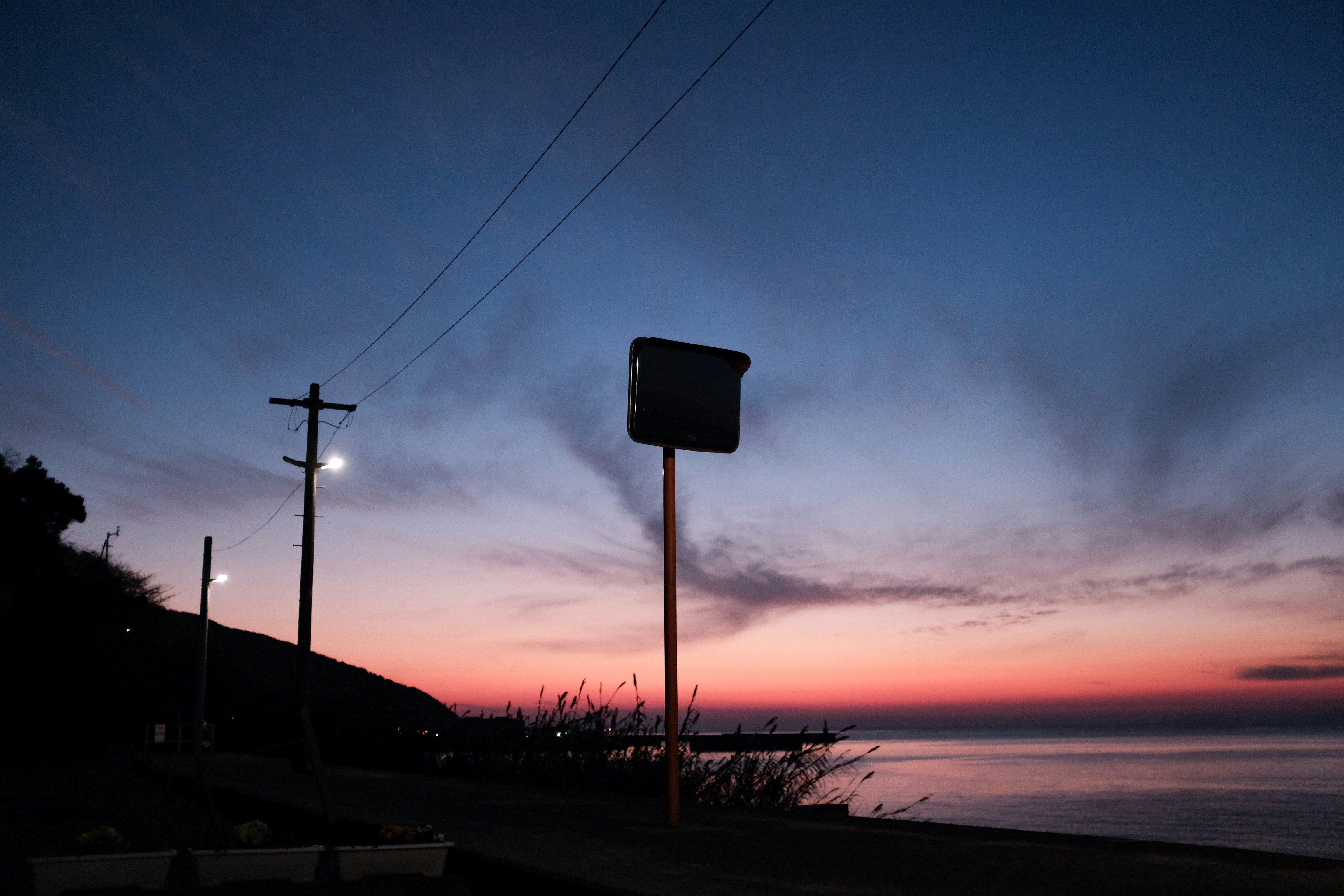 Lone Road Sign at Dusk: A Quiet Coastline Painted in Coral and Indigo
