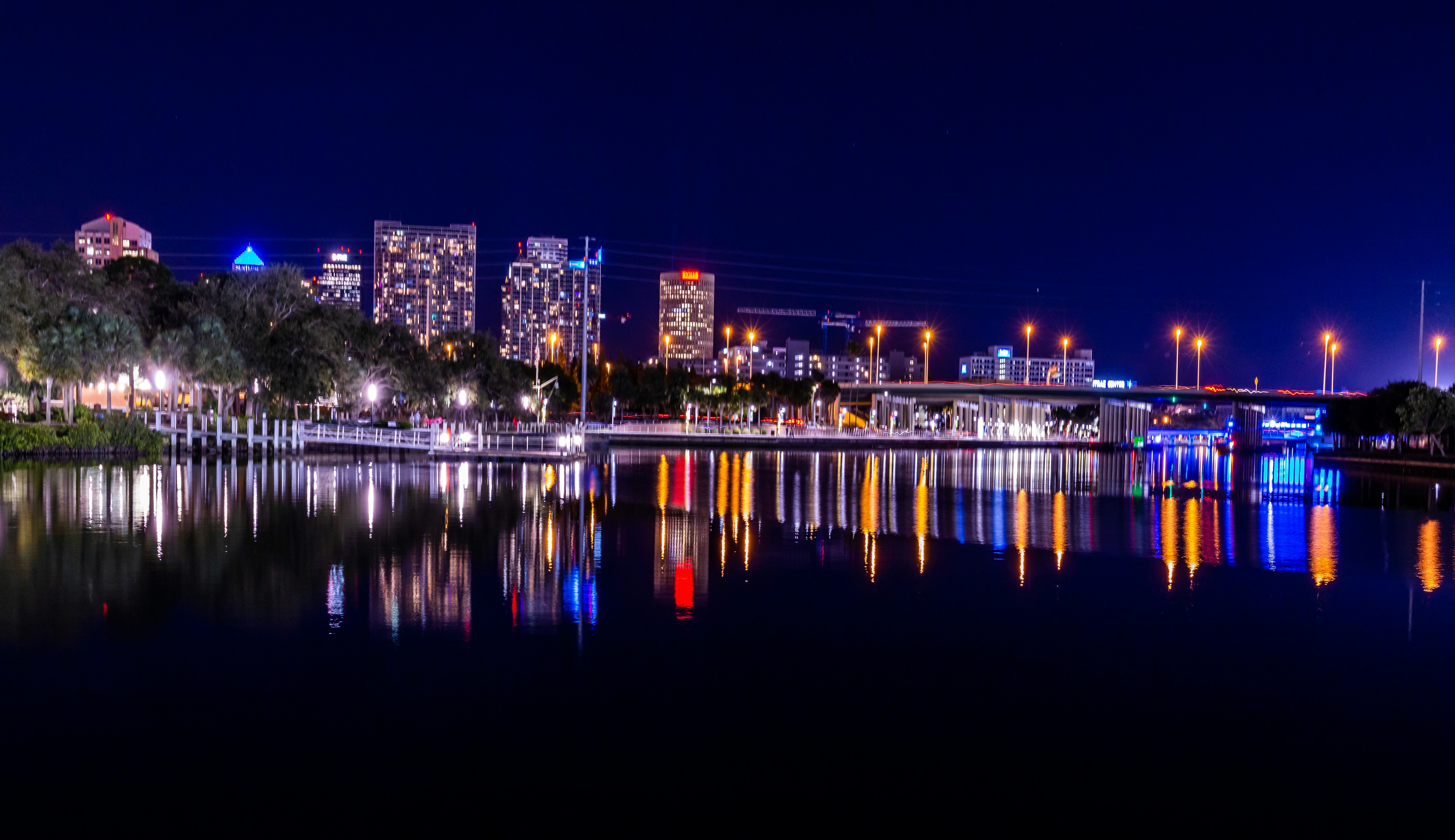 City skyline illuminated at night with colorful reflections on the water.