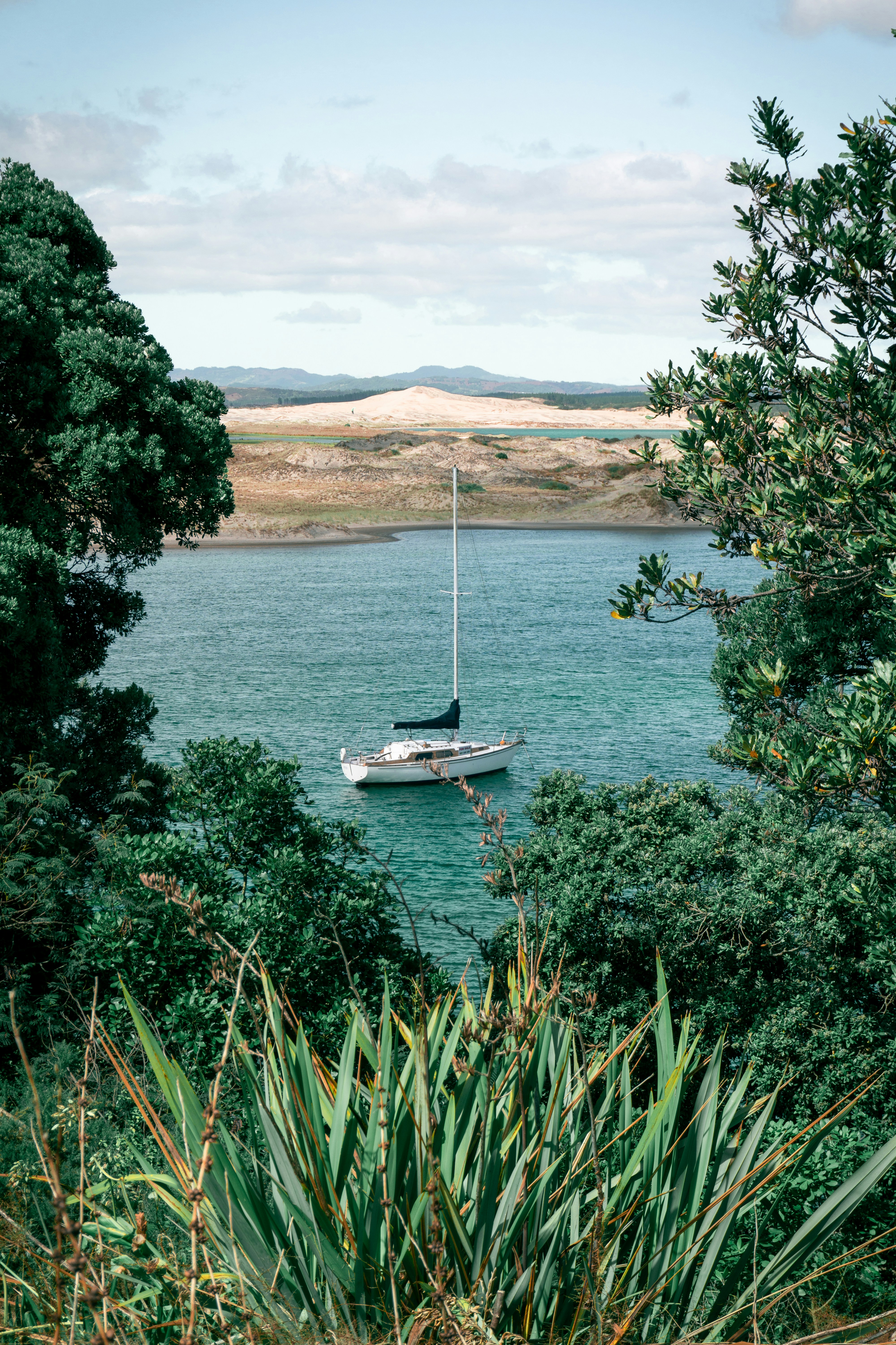 A sailboat anchored in a tranquil bay, surrounded by lush greenery and distant hills under a clear sky.