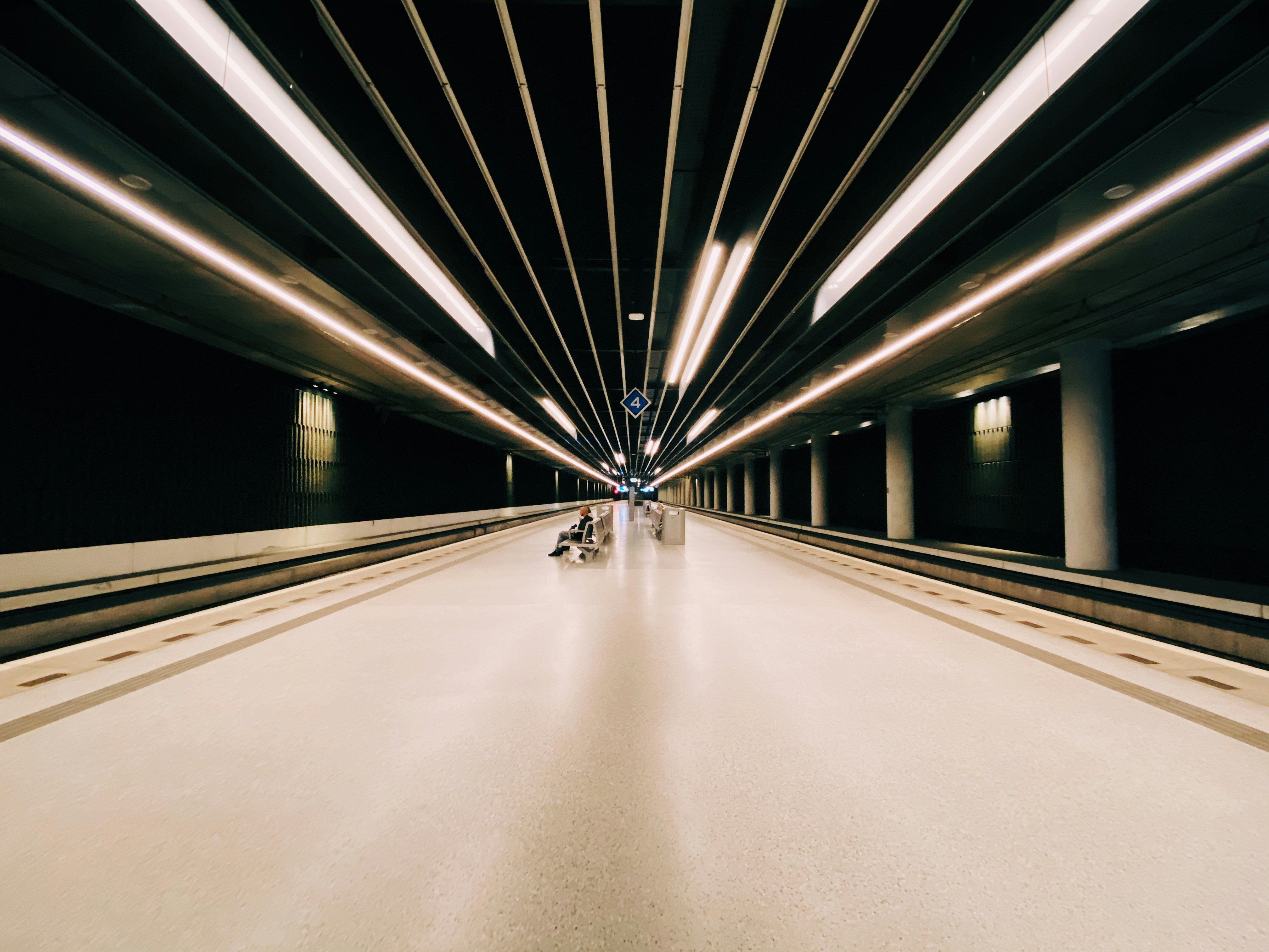 Empty underground train platform with converging ceiling lights creating a tunnel effect.
