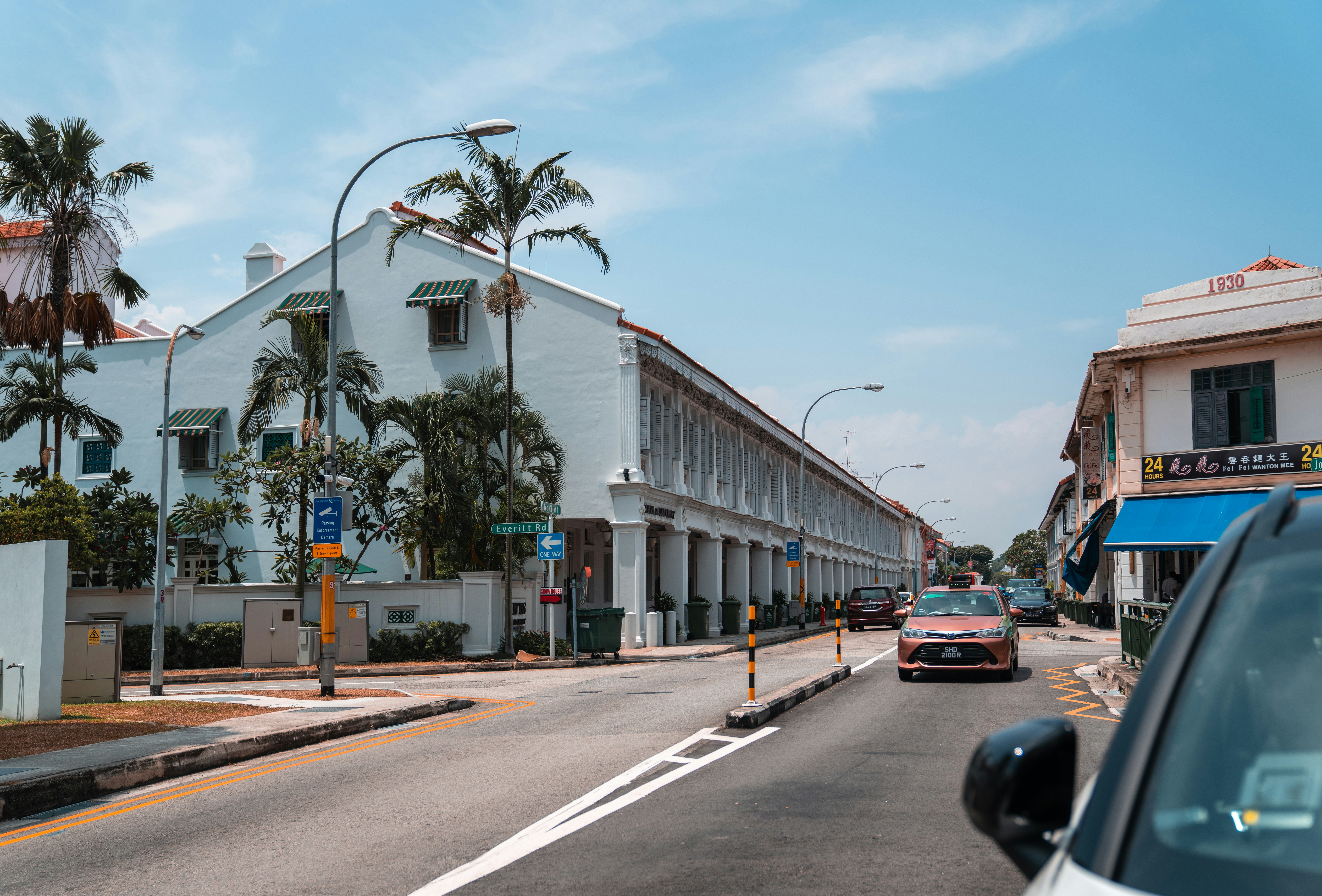 Charming street scene showcasing colonial-style architecture with palm trees lining the road and a red car navigating the urban landscape.