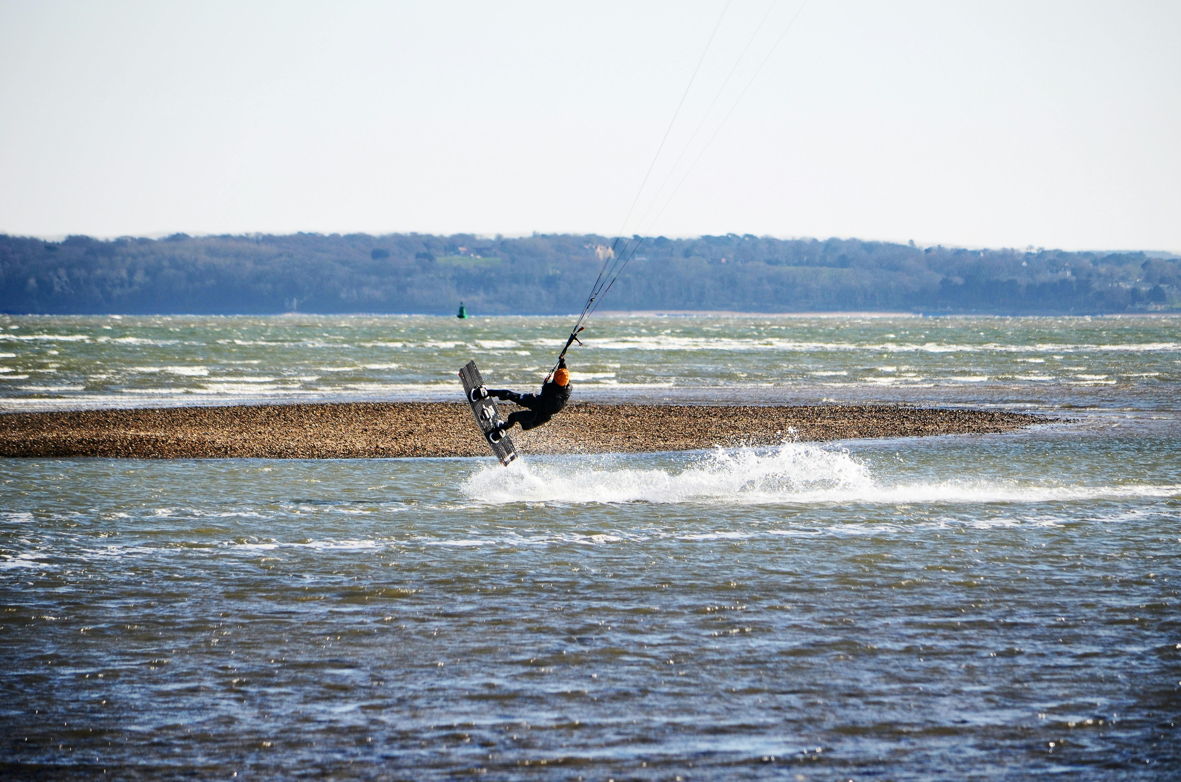 Kitesurfer executing a high jump above choppy sea near a sandy shoreline.