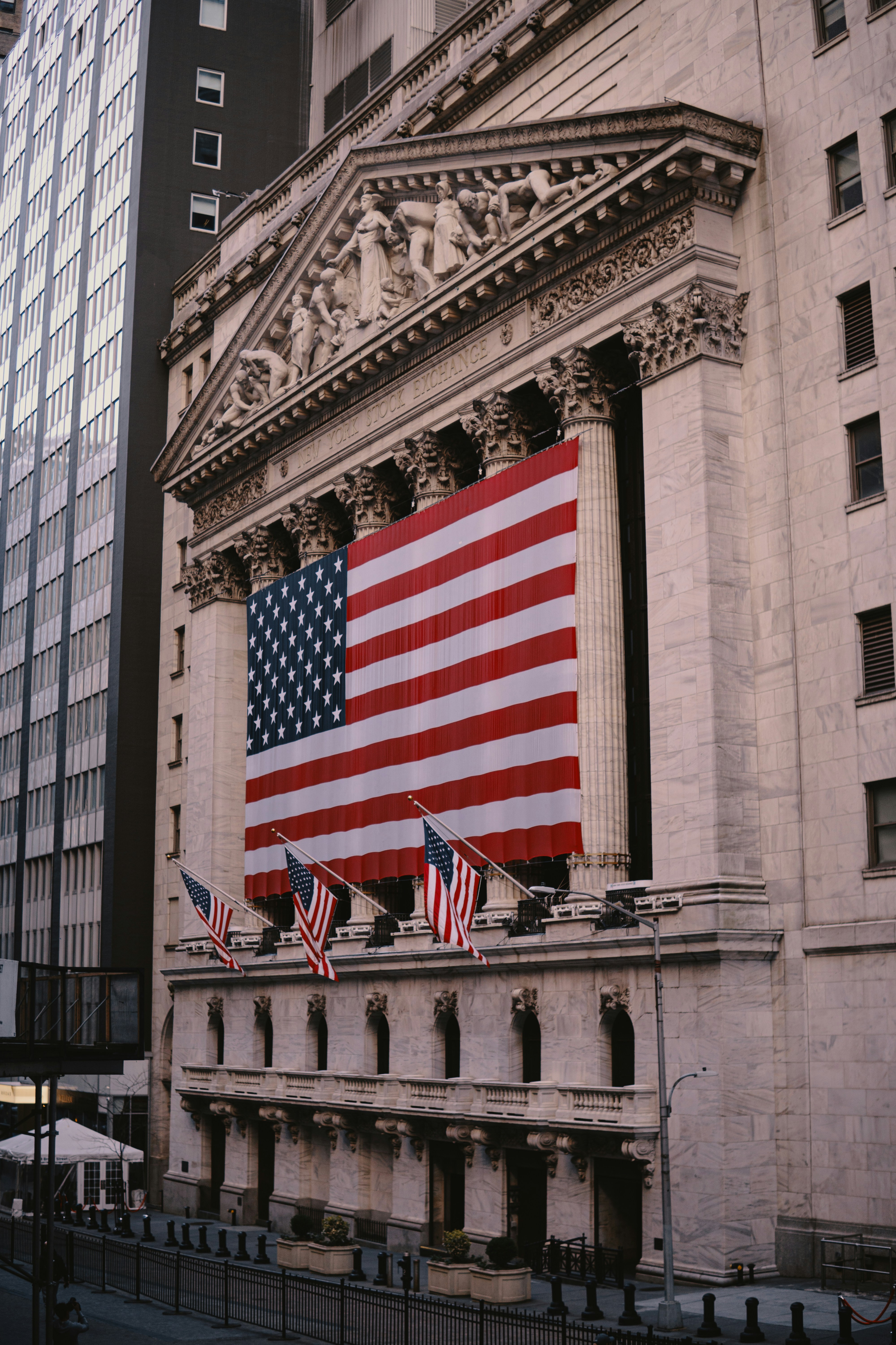 The New York Stock Exchange adorned with a large American flag, flanked by smaller flags, showcasing a blend of architectural grandeur and national pride.