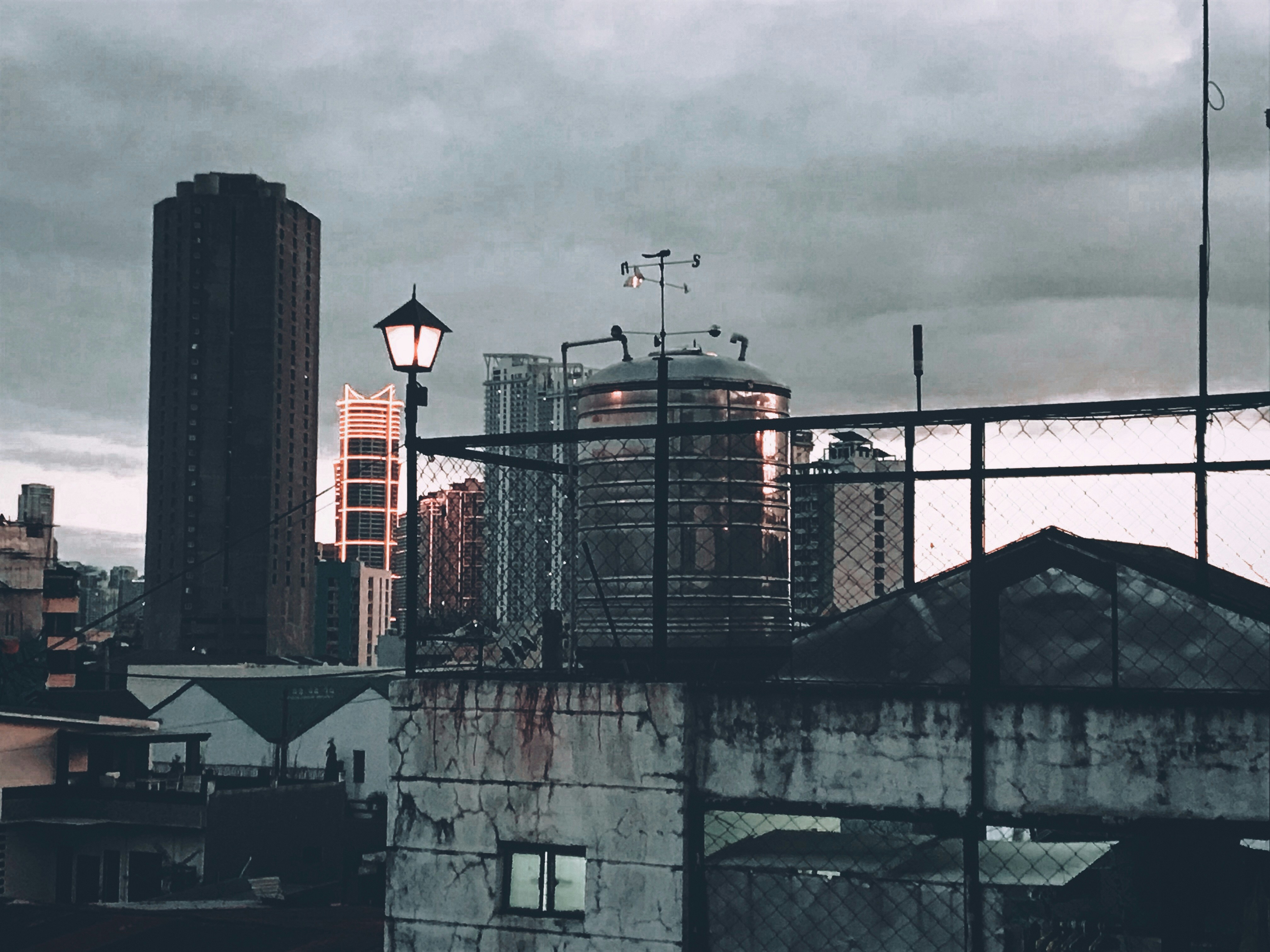 City skyline with modern buildings and a vintage lamppost, captured during twilight. A metallic water tank contrasts with the urban landscape.