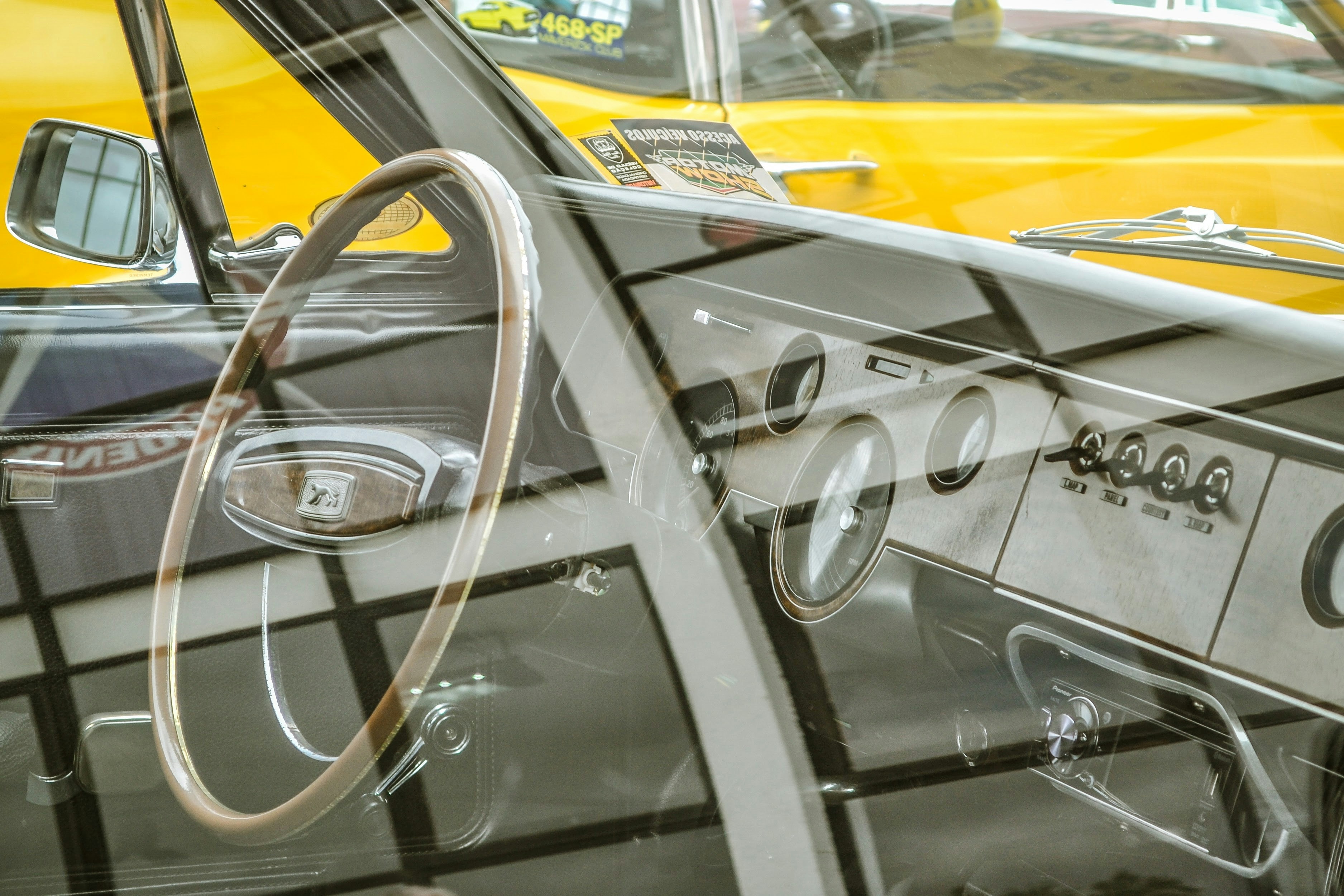 Classic car interior with a wooden steering wheel and dashboard dials, reflected in a glossy window.