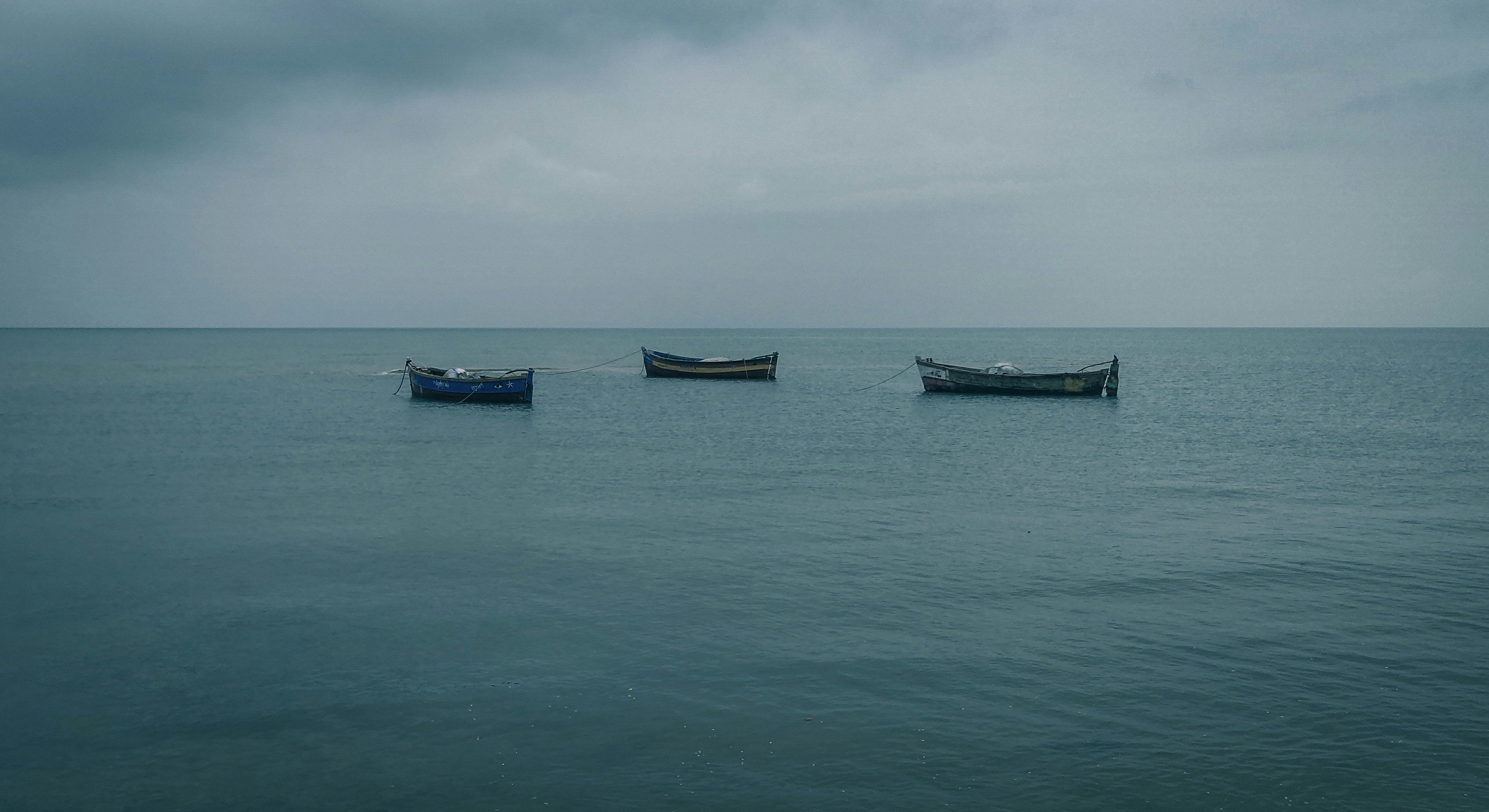 Three boats floating in calm, overcast waters under a moody sky.