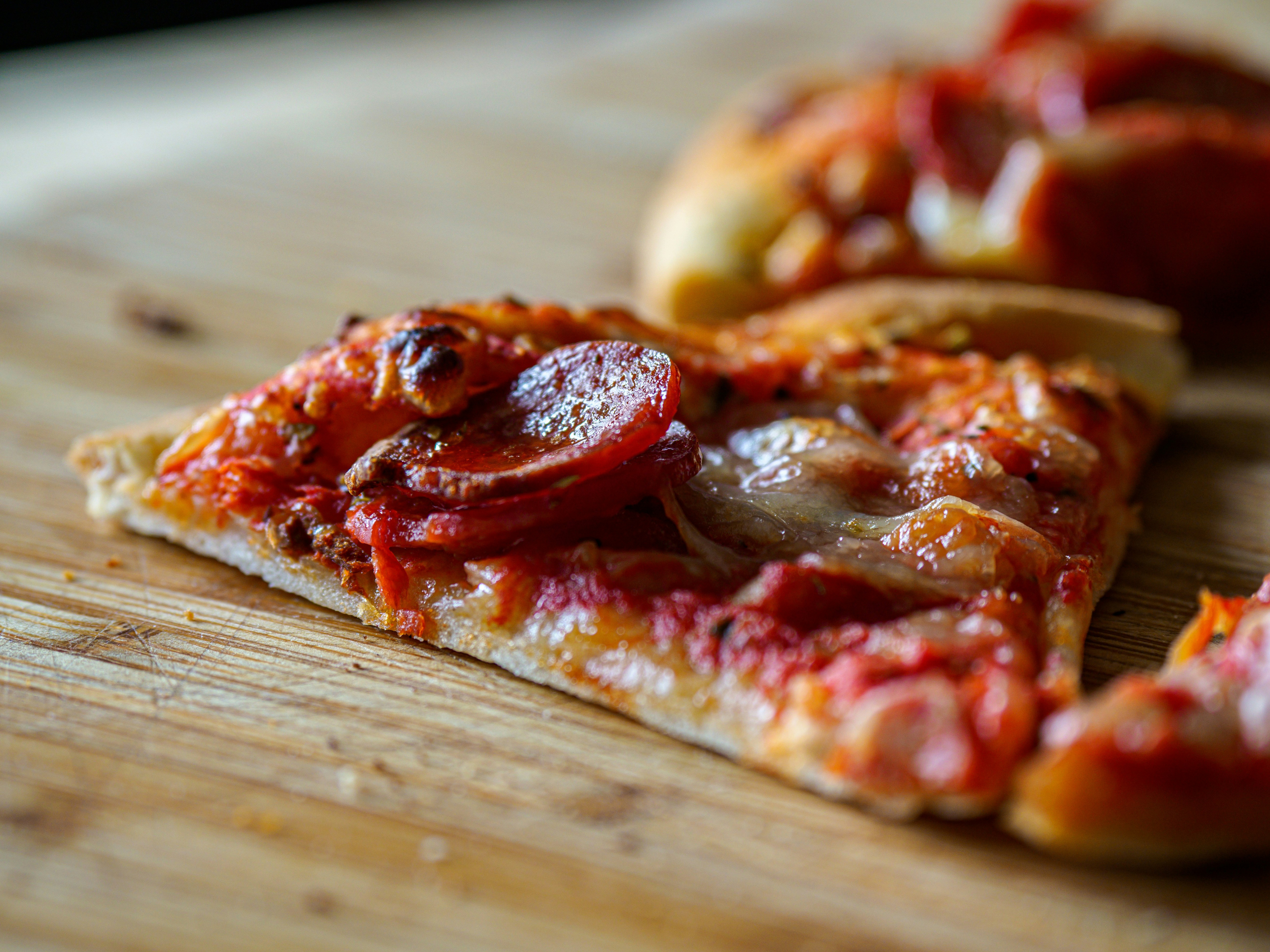 Close-up of a pepperoni pizza slice resting on a wooden cutting board, showcasing its melted cheese and toppings.