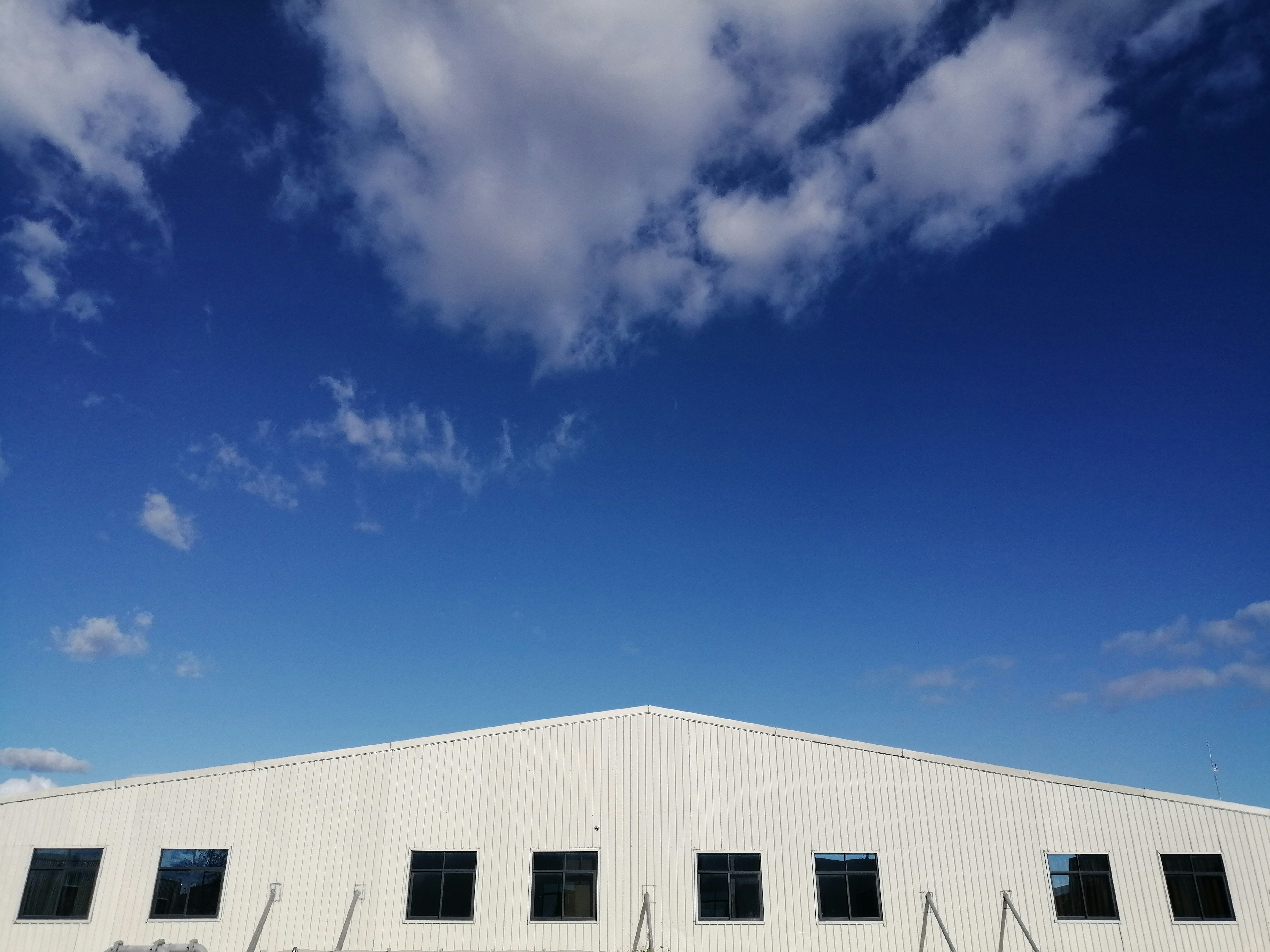 White industrial building against a clear blue sky with scattered clouds.