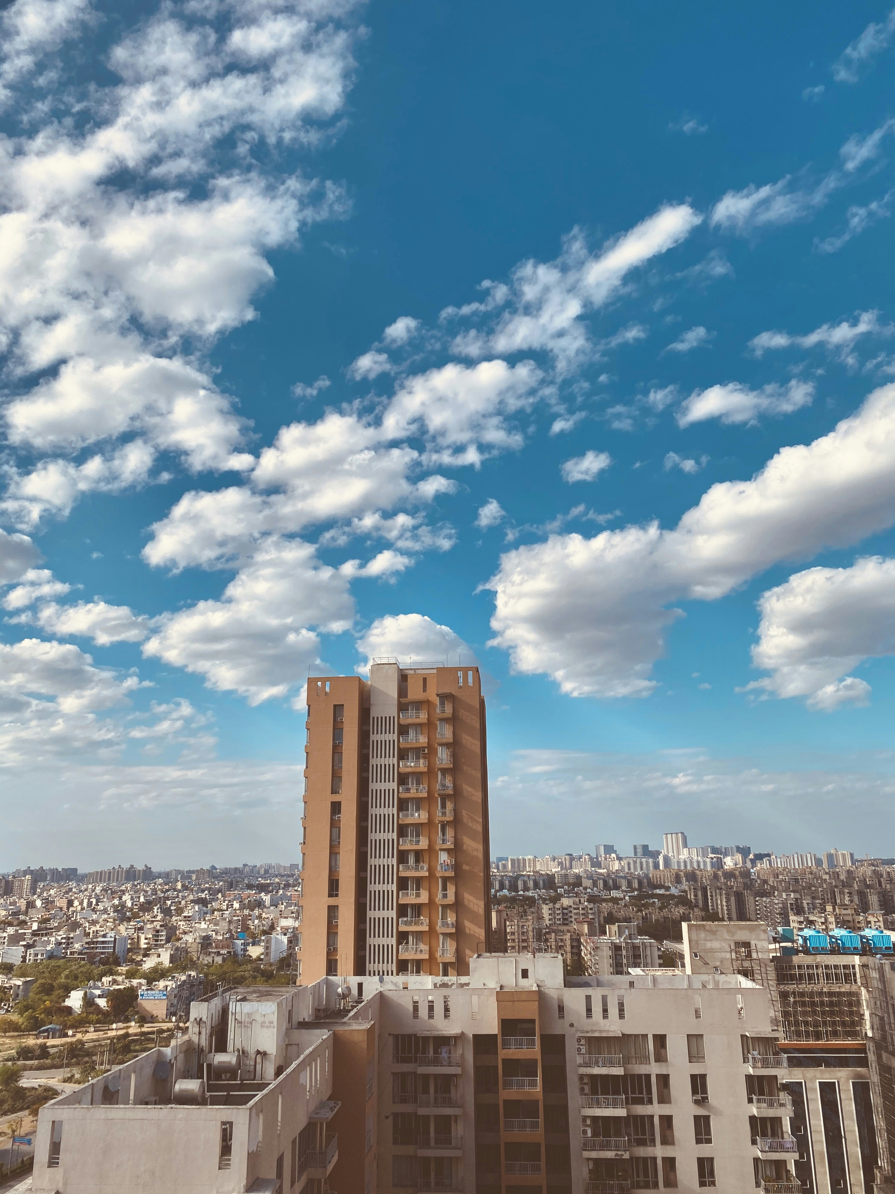 A high-rise building stands prominently against a backdrop of fluffy clouds and a vibrant blue sky, showcasing an urban landscape. The scene captures the essence of city life and atmospheric beauty.