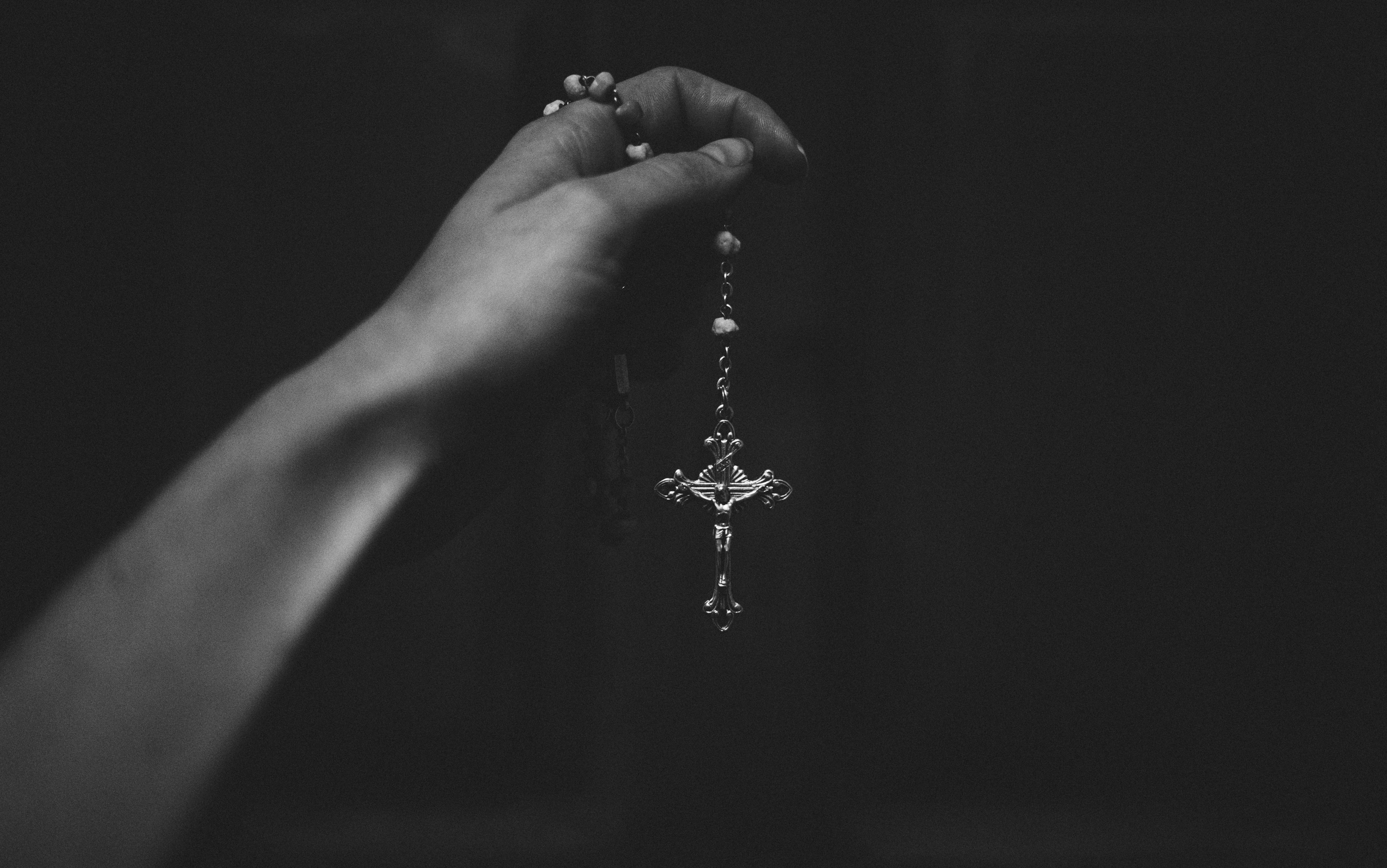 A hand gripping a rosary with a silver crucifix against a dark background, symbolizing faith and contemplation.