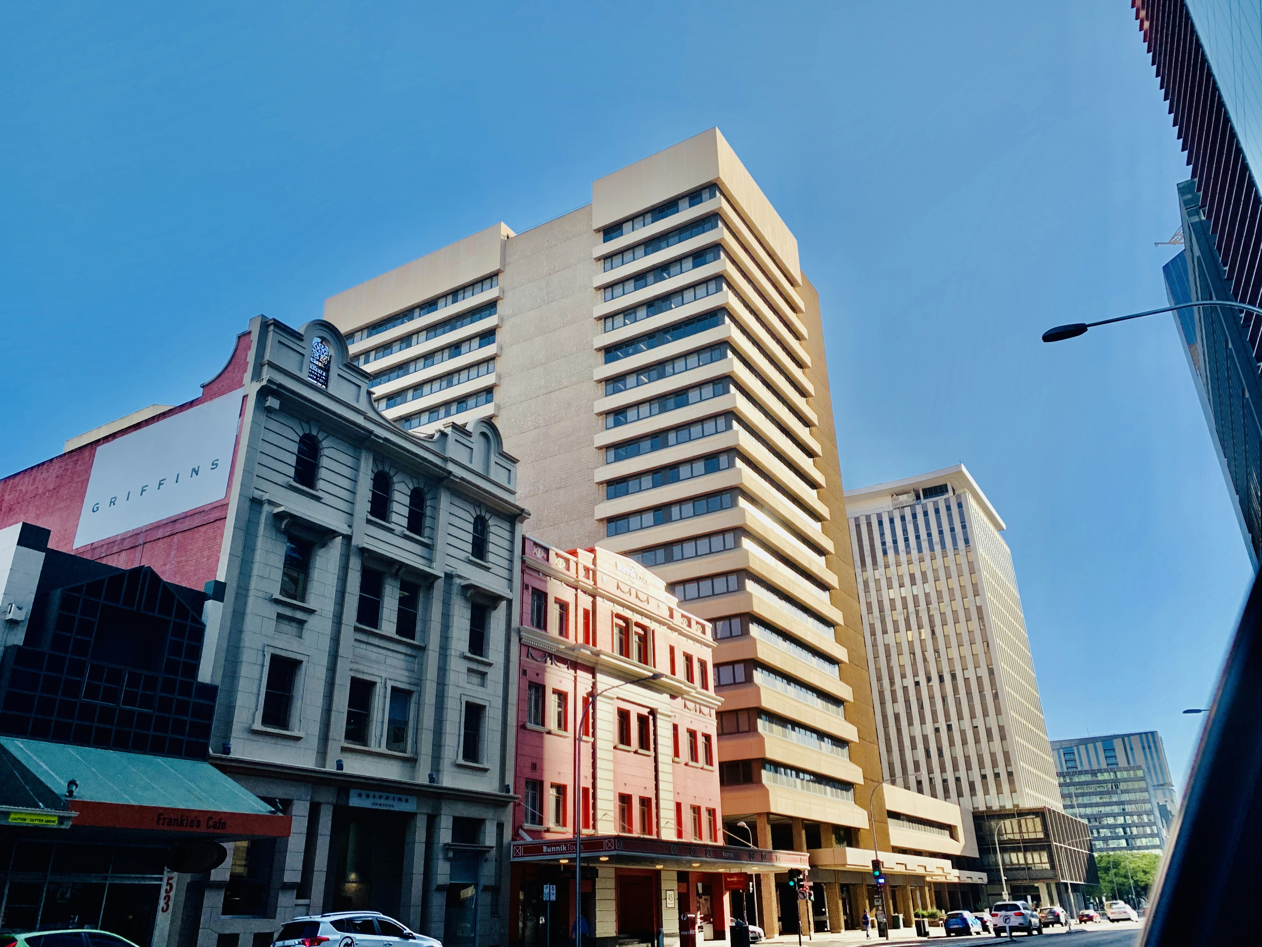 Historic and modern buildings converge in a vibrant cityscape, showcasing diverse architectural influences. Clear blue sky serves as a backdrop.