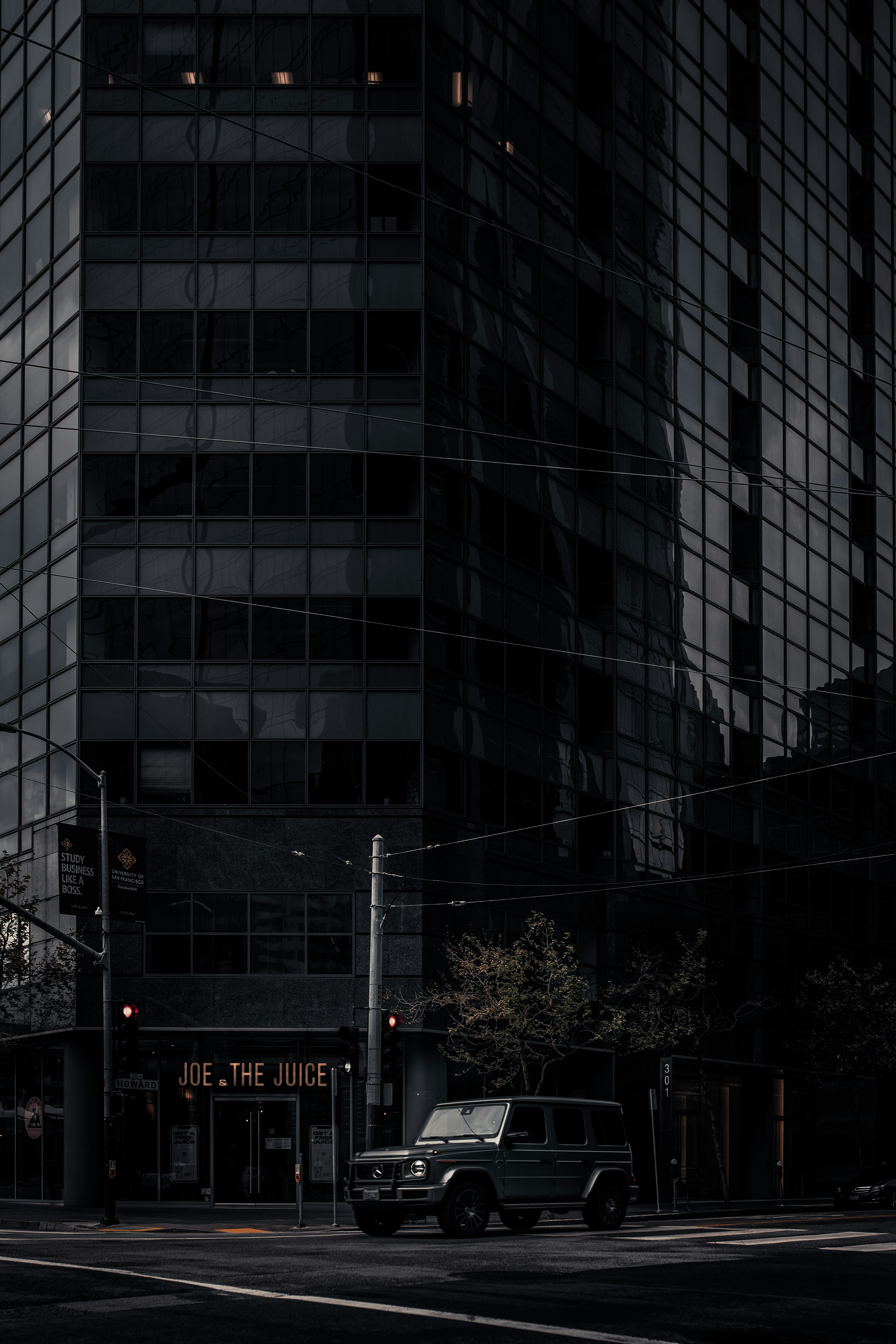 A sleek SUV parked at a street corner, framed by a reflective glass building and dimly lit urban surroundings.