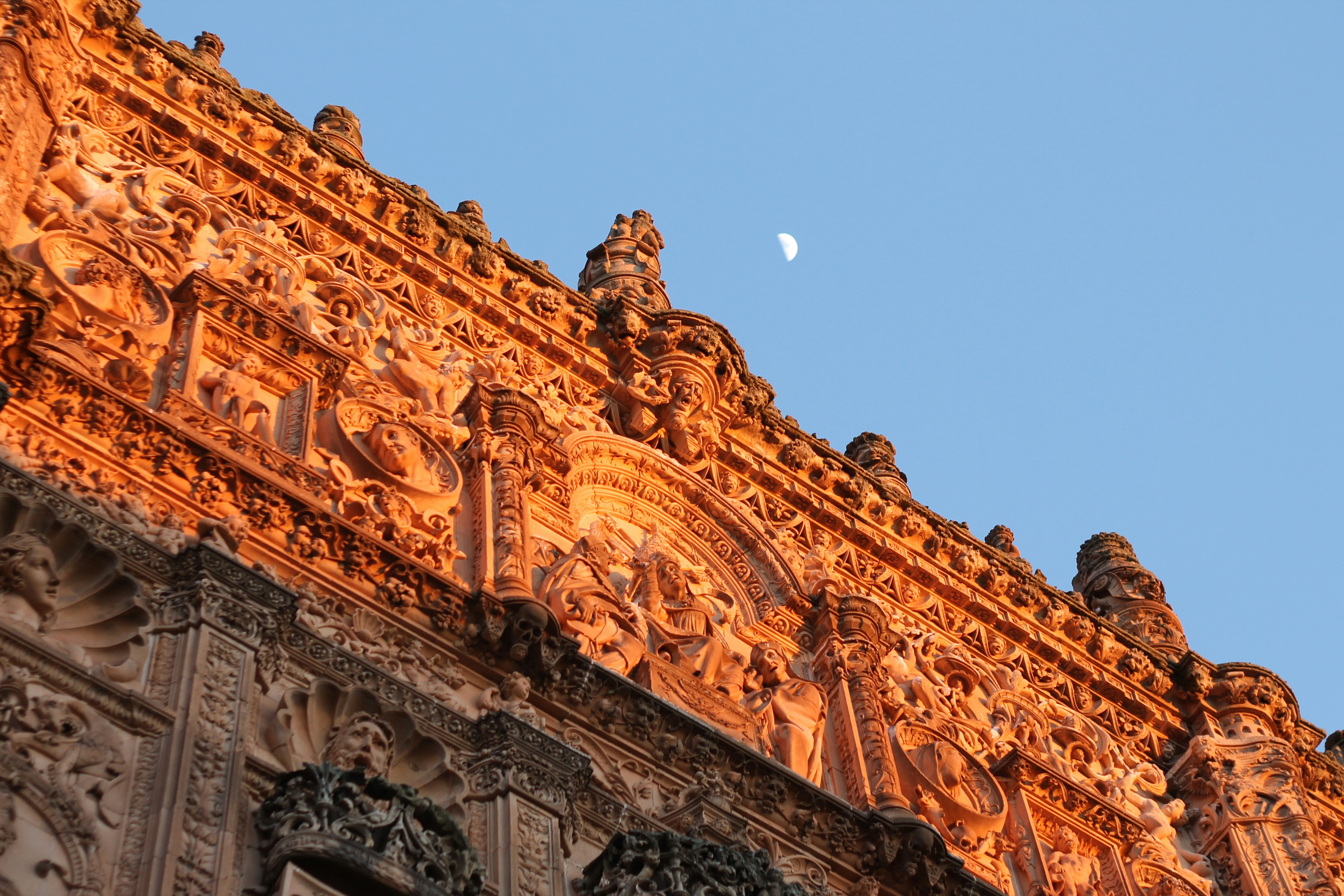Sunlit Frieze: Carved Stone Facade Under a Distant Moon