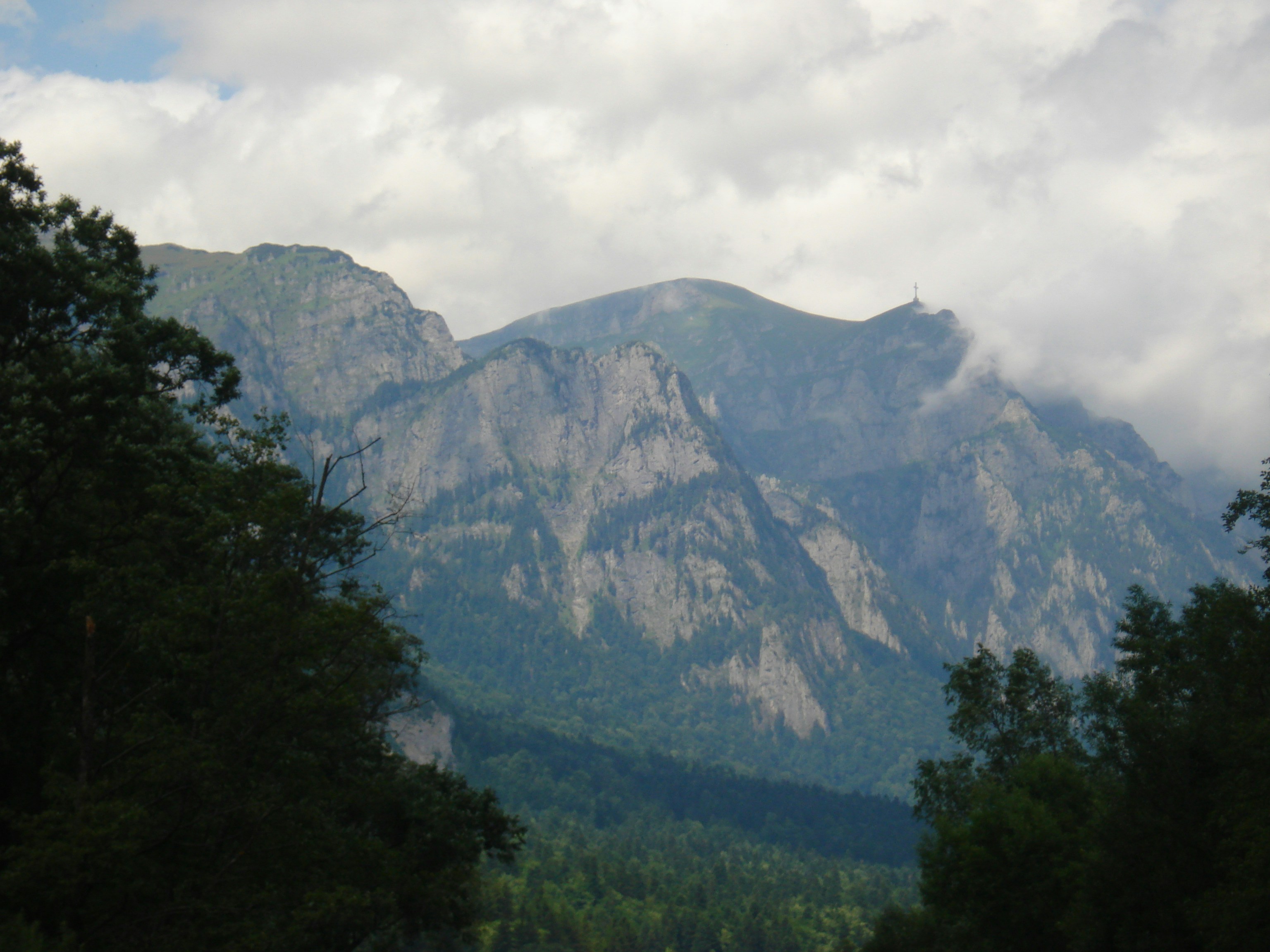 Majestic mountain range shrouded in clouds, framed by lush greenery in the foreground. The scene evokes a sense of tranquility and adventure.