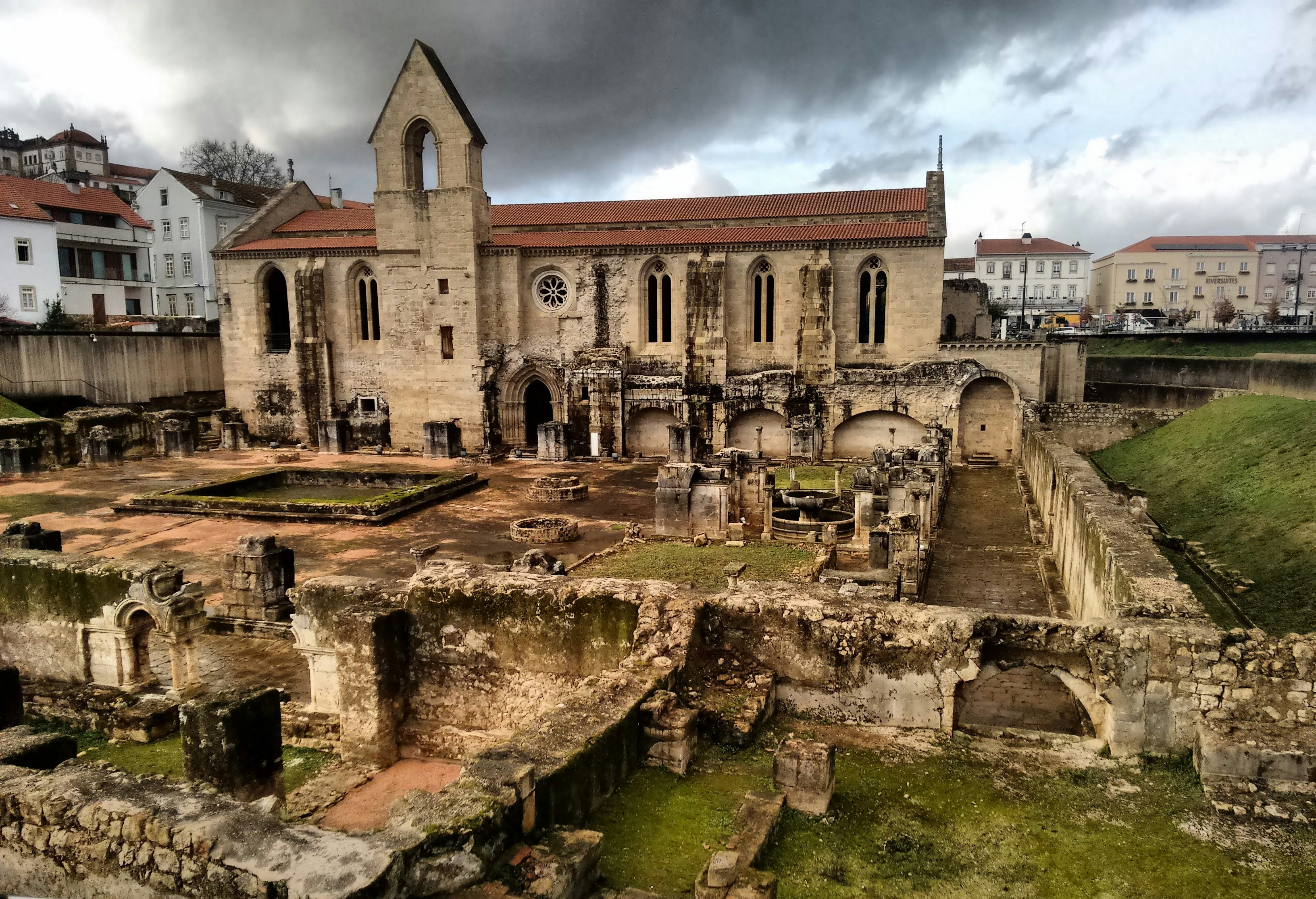 Ruins of a medieval convent with weathered stone structures under a dramatic cloudy sky.