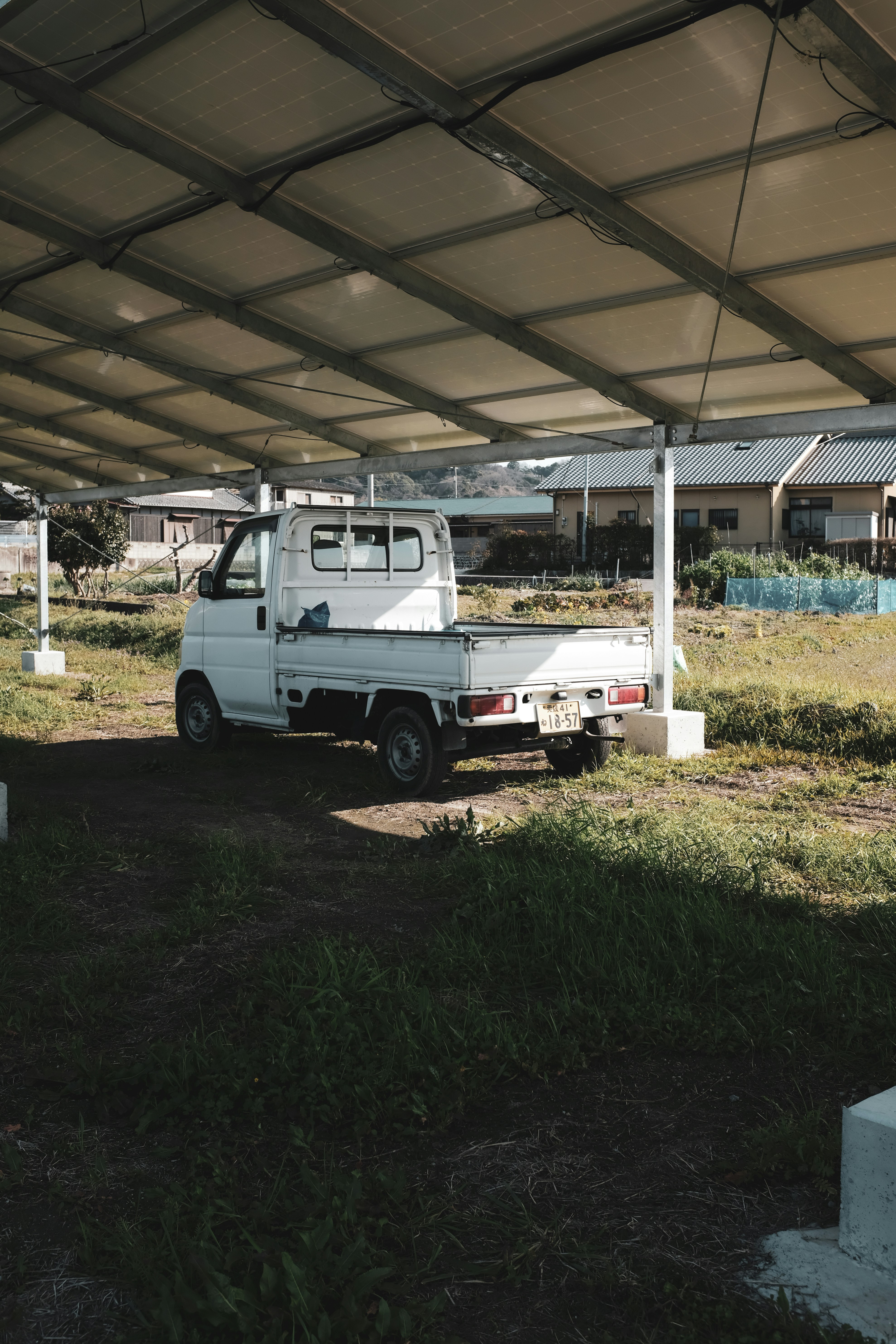 White Pickup Resting Under a Corrugated Canopy in a Quiet Rural Yard