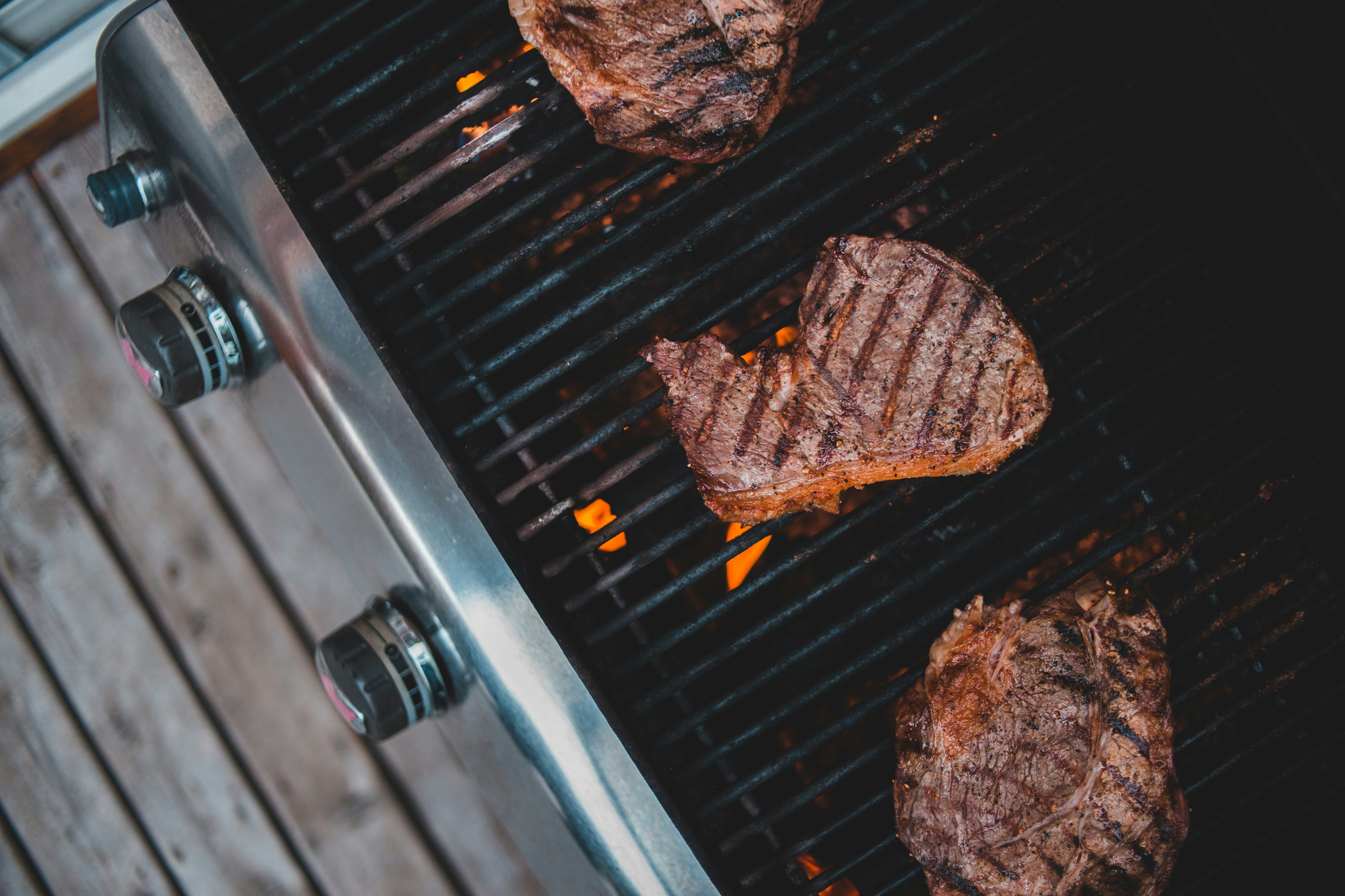 Grilled steaks with perfect sear marks resting on a barbecue grill, surrounded by glowing embers.