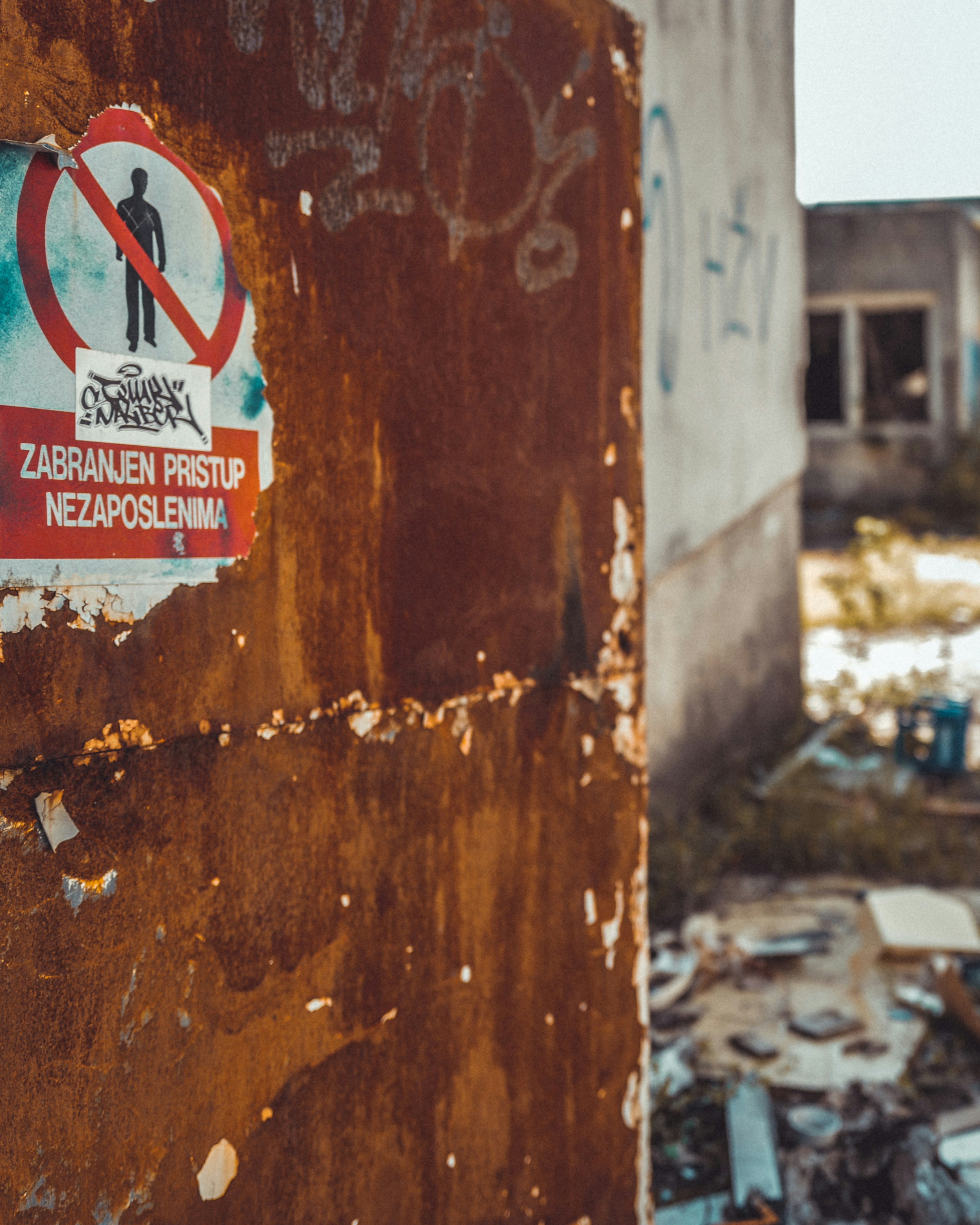 A weathered 'No Entry' sign affixed to a rusty wall in an abandoned building, surrounded by remnants of neglect.