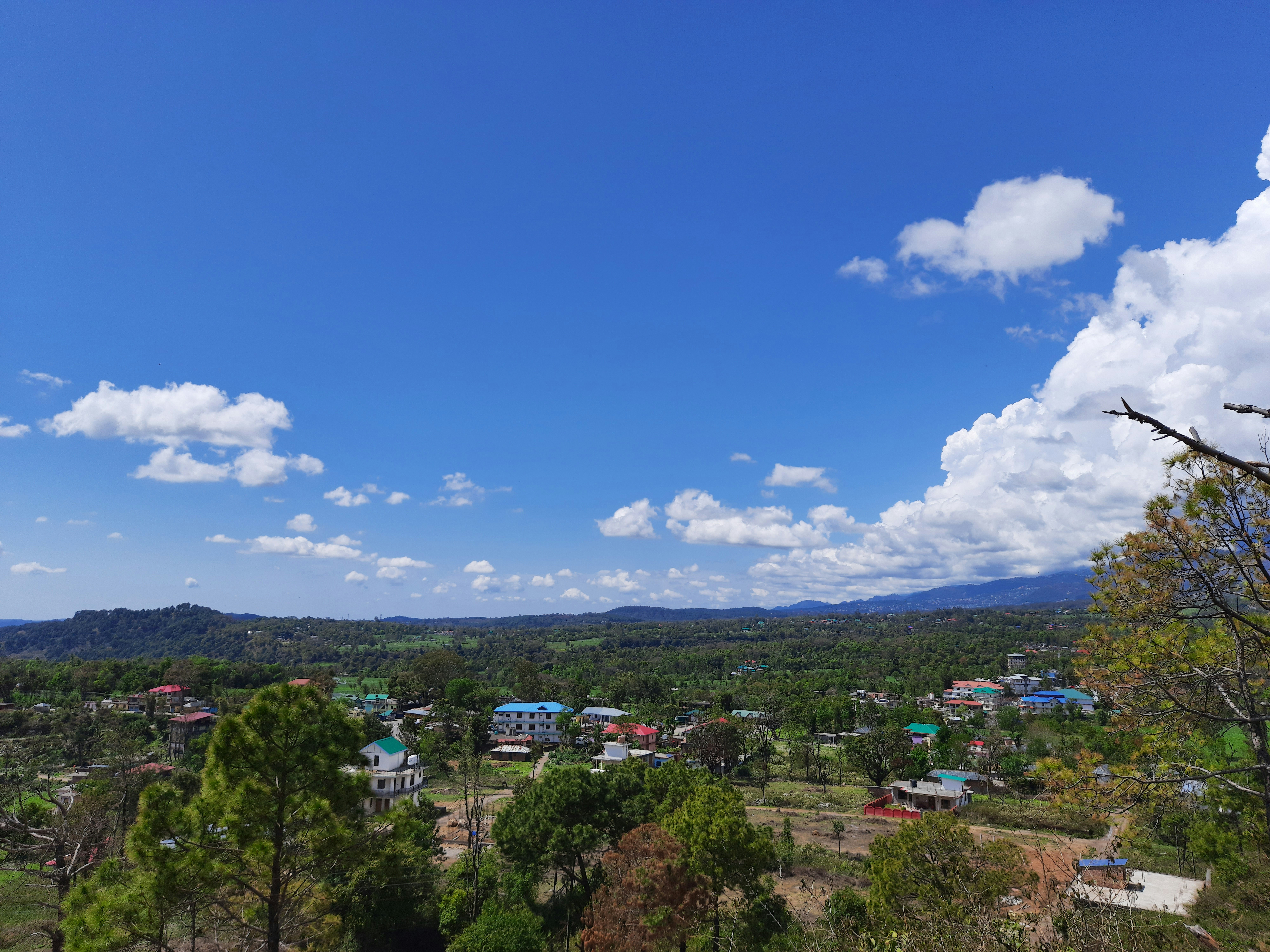 Vibrant landscape showcasing a mix of lush greenery and colorful houses under a bright blue sky with scattered clouds.