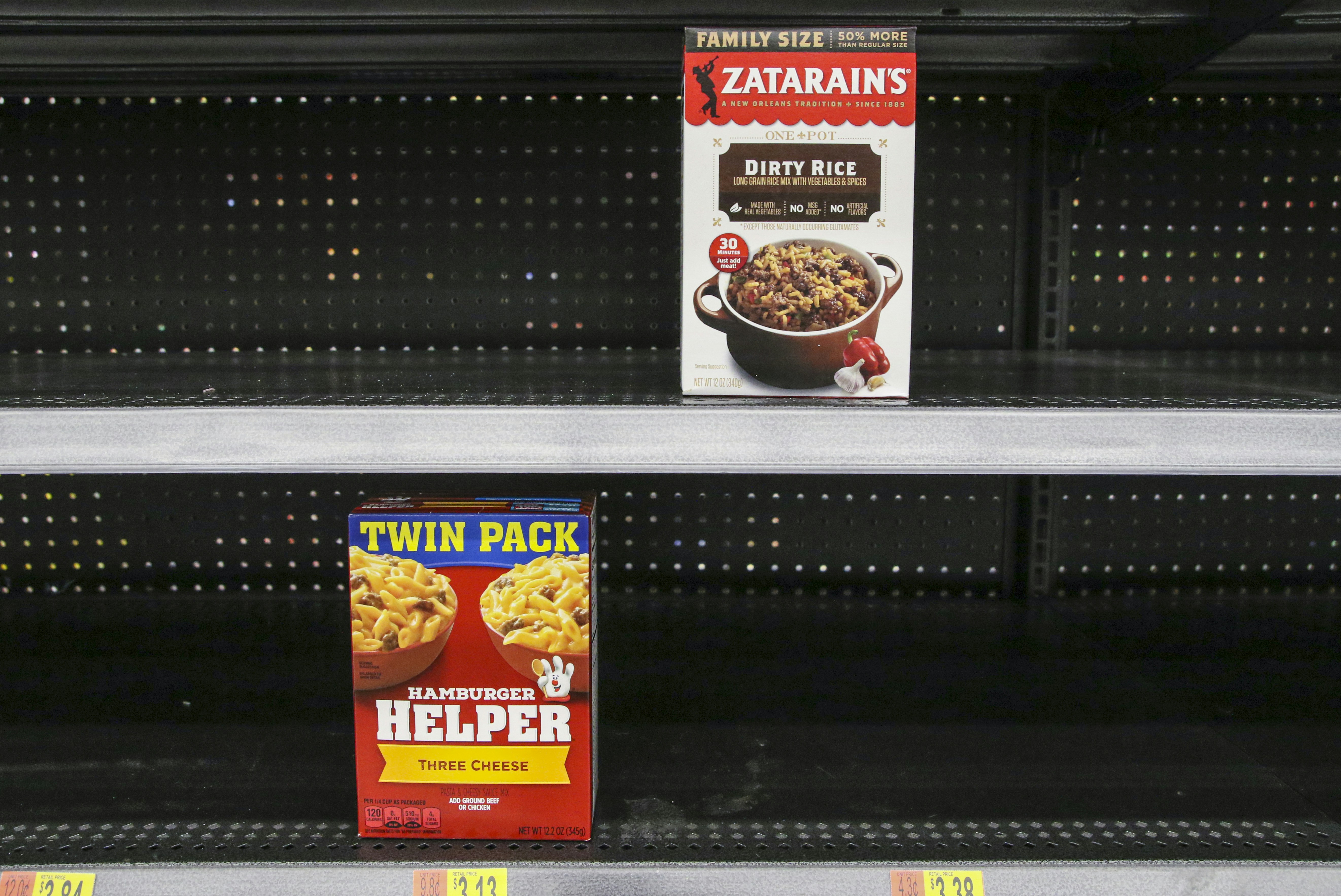 Two boxed meal products on a nearly empty grocery shelf, highlighting the scarcity of food options. The focus is on Zatarain's Dirty Rice and Hamburger Helper in a twin pack.