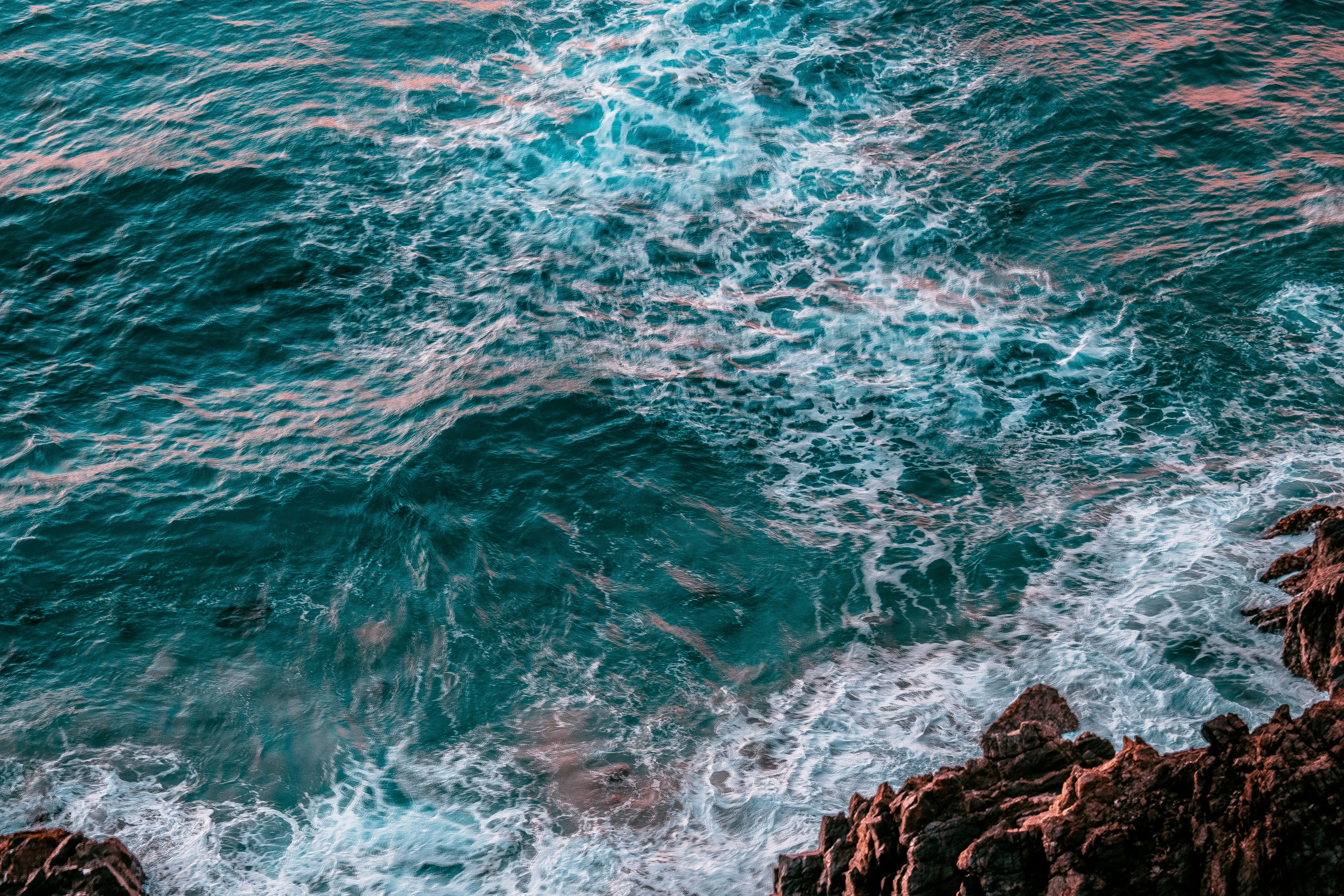 Vibrant turquoise waves crash against rugged coastal rocks, creating a dynamic interplay of water and stone.