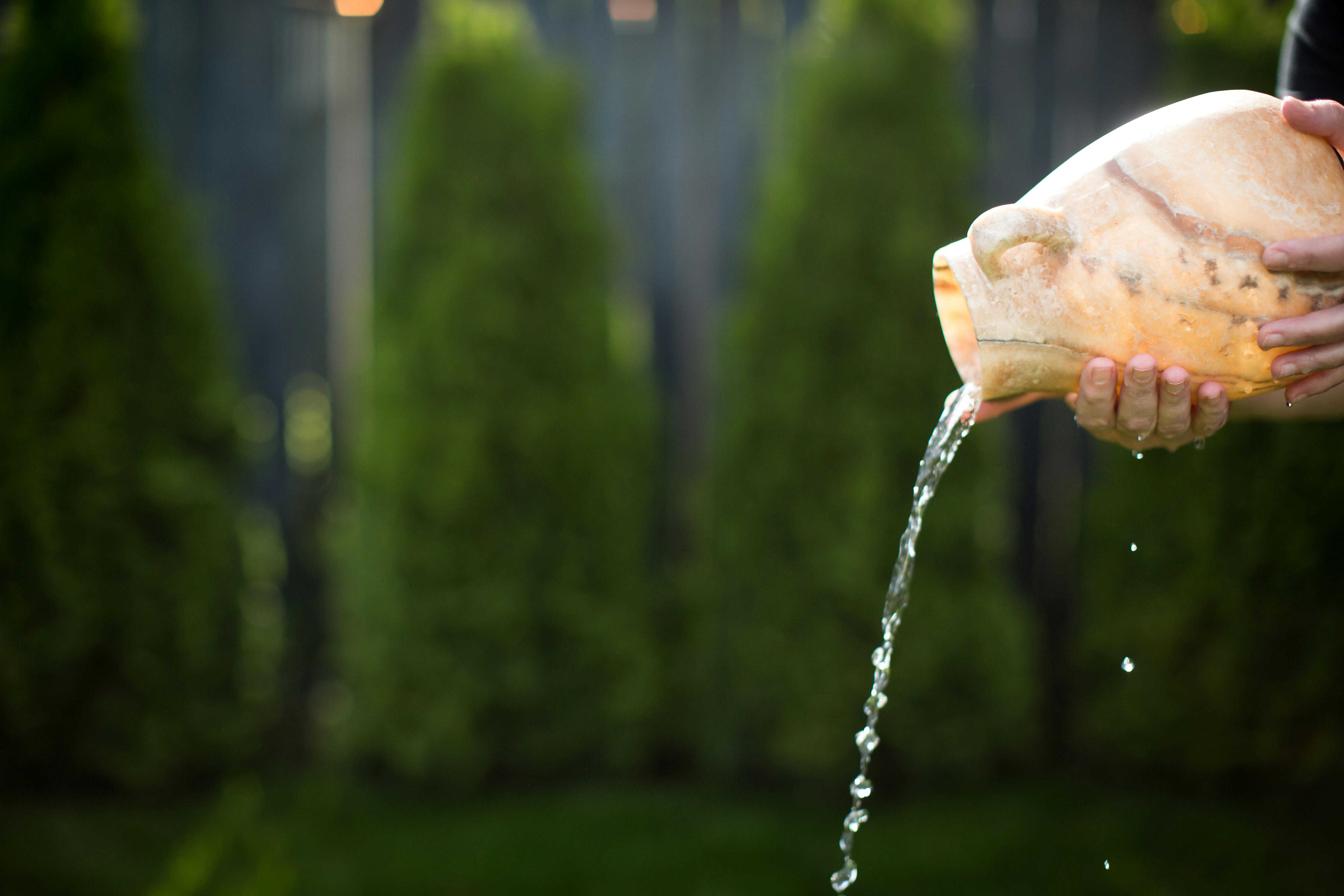 Water cascading from an alabaster jar against a backdrop of lush greenery.