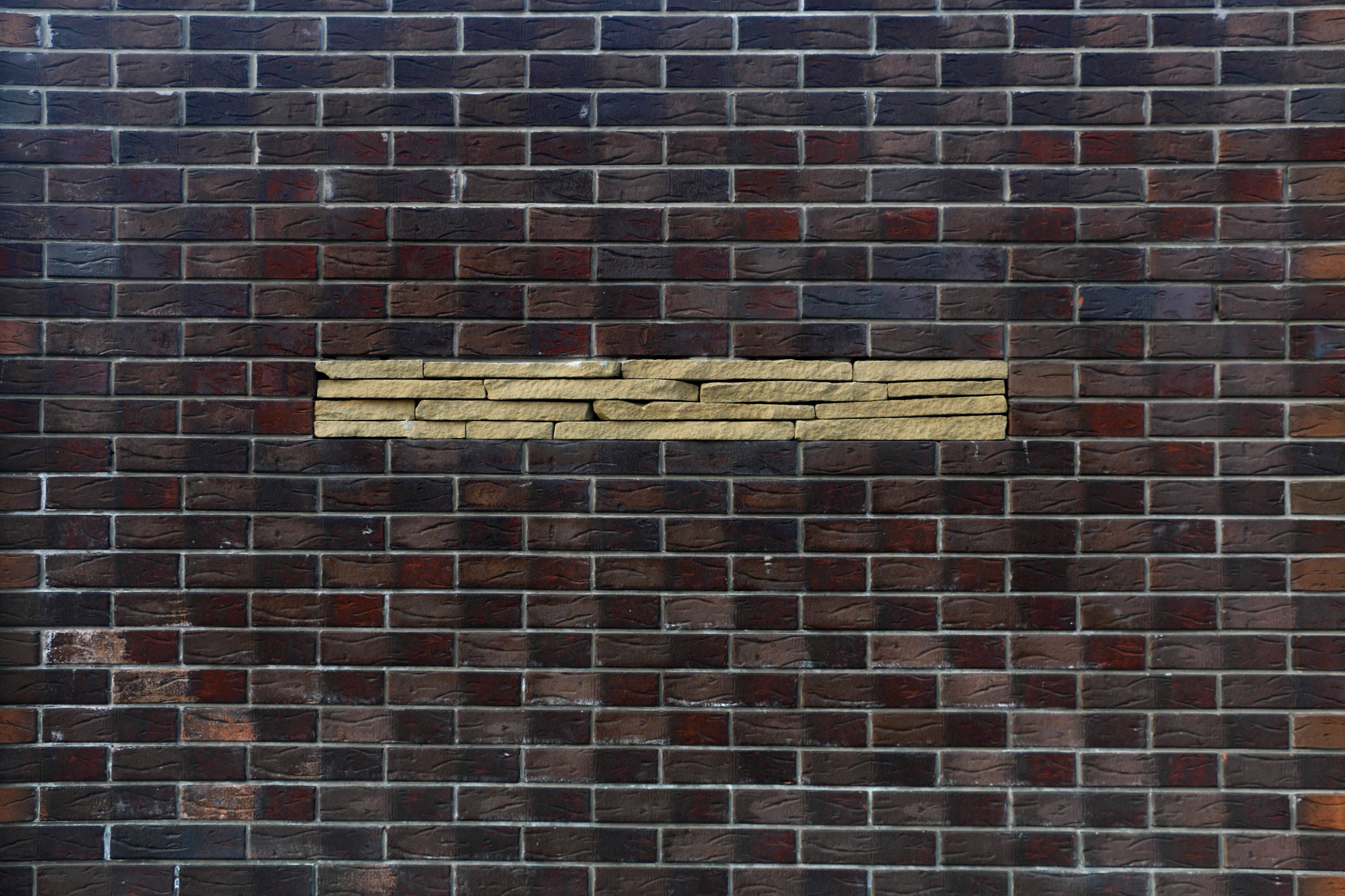 A section of a brick wall featuring a distinct, smooth stone strip that contrasts with the rough texture of the surrounding bricks.