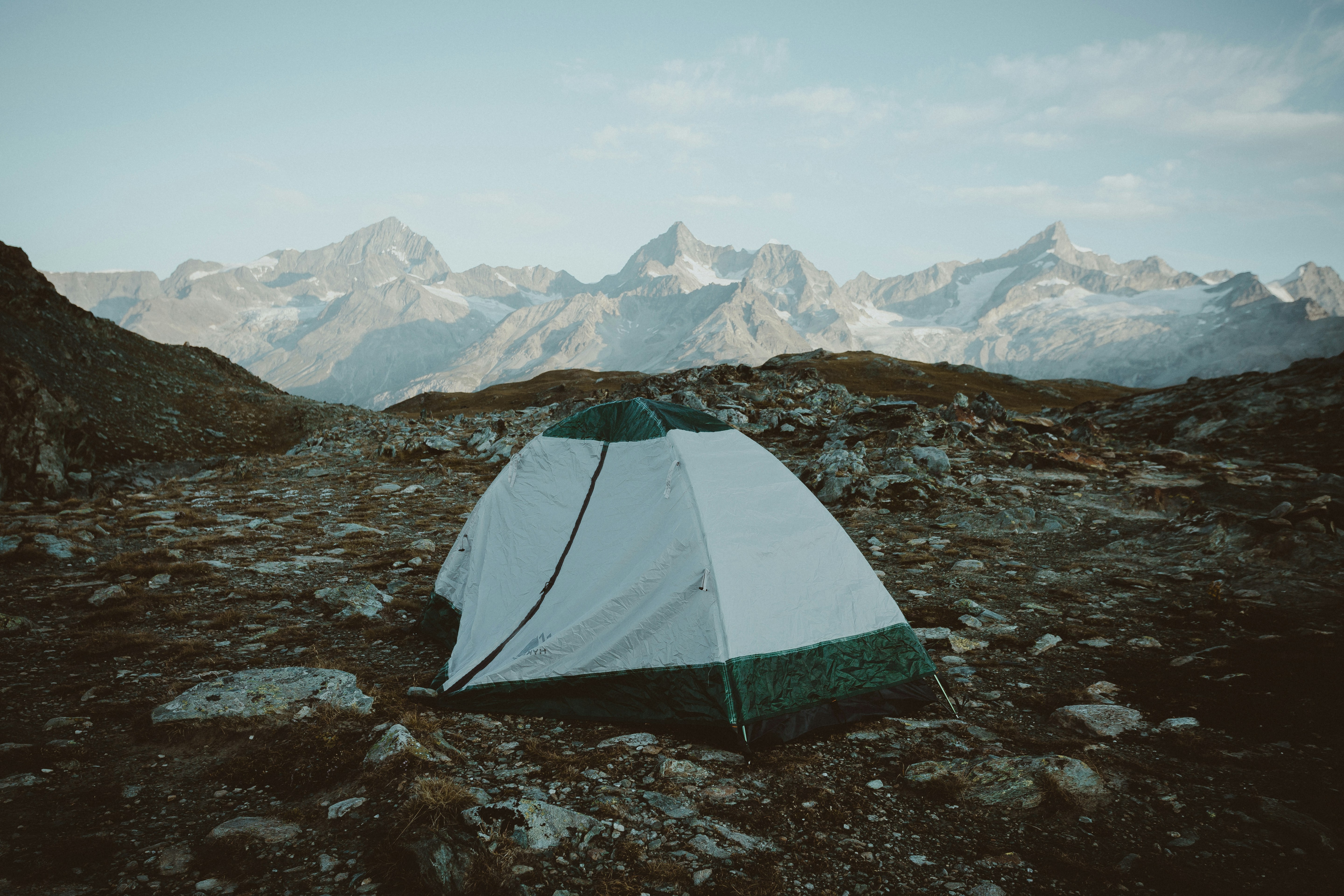 A tent nestled among rocky terrain with towering mountains in the background, showcasing the beauty of nature's wilderness.