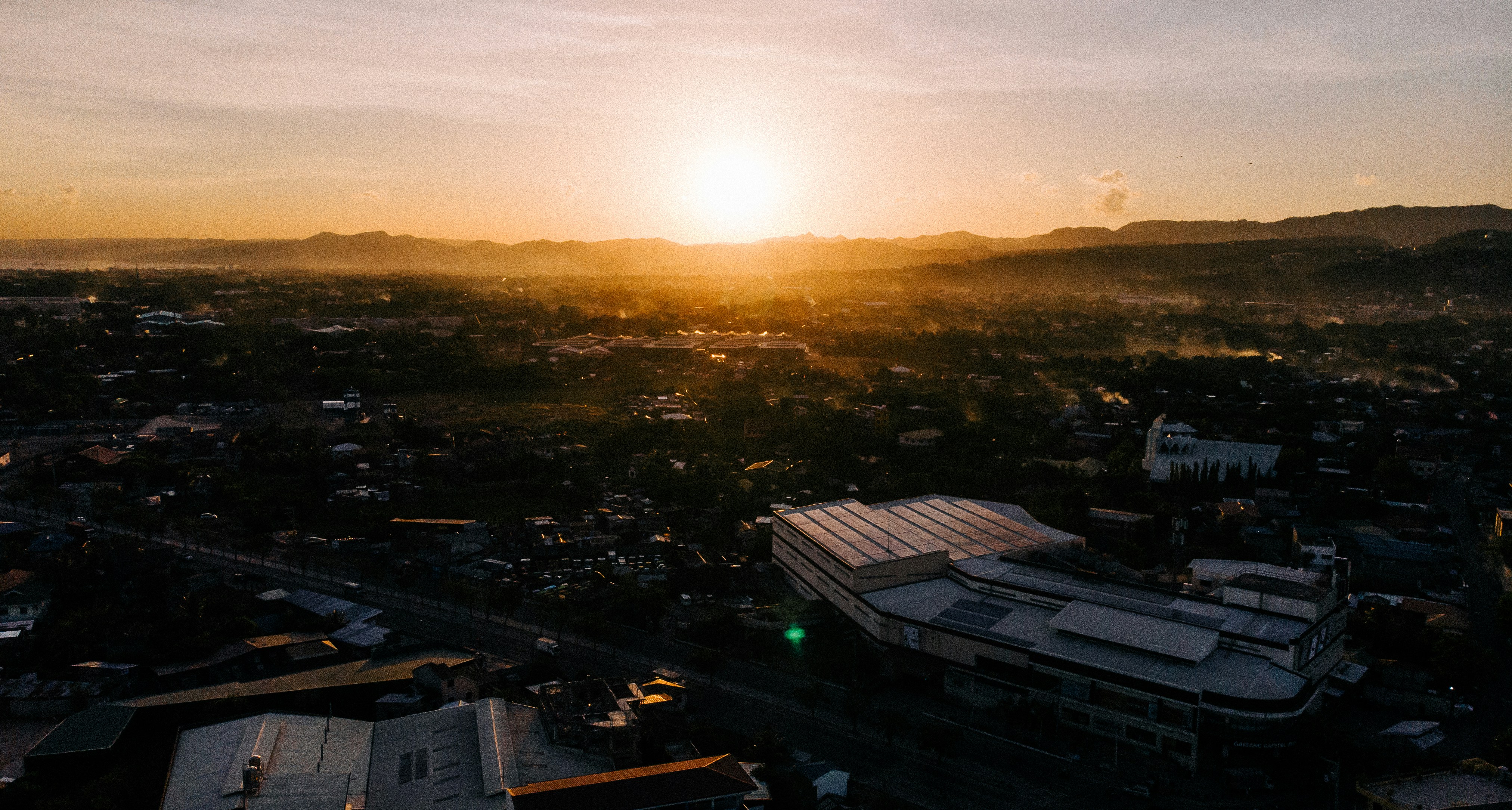 Sun setting over a bustling community with silhouetted buildings and soft evening light.