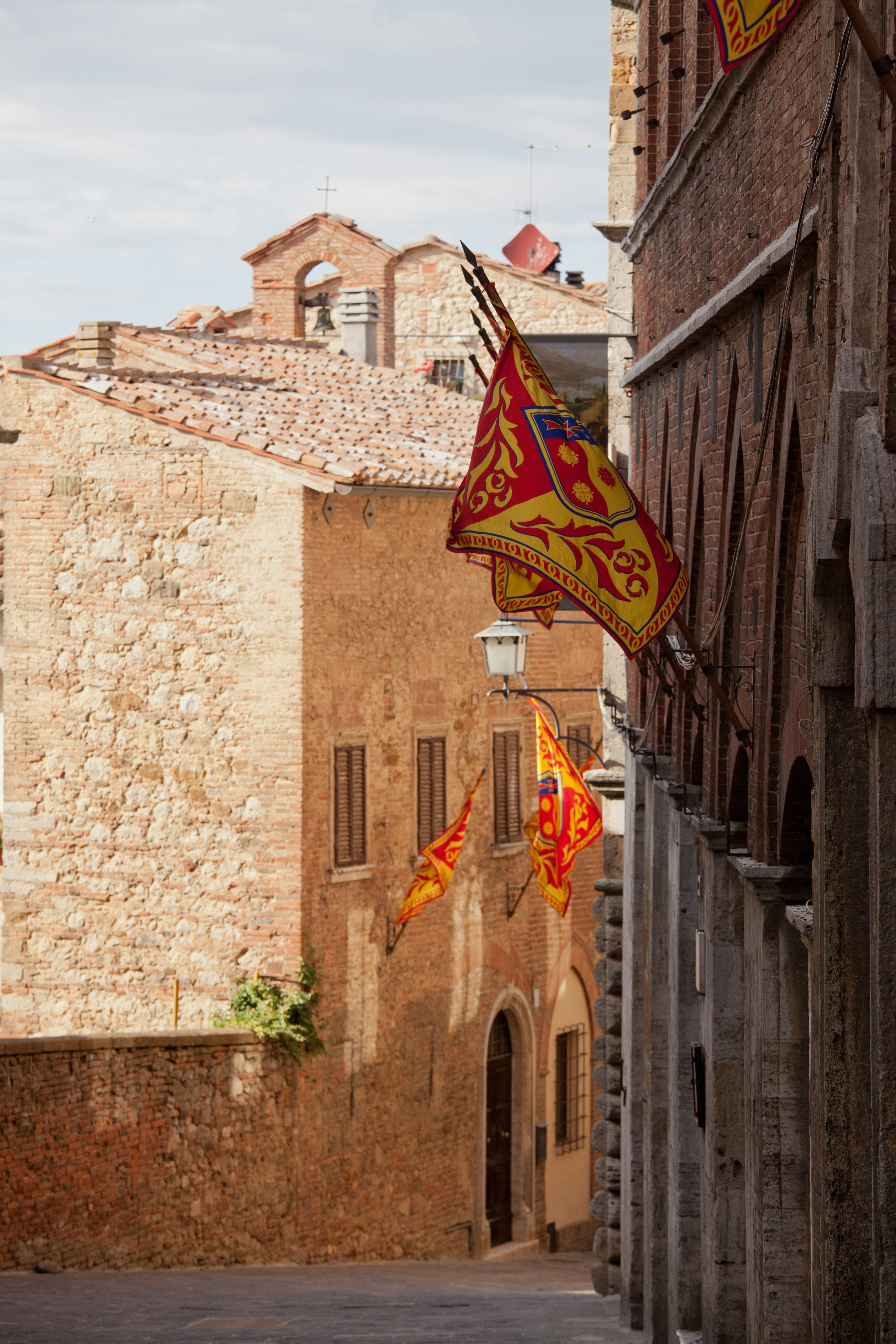 Sunlit medieval street awash with crimson-yellow heraldic banners