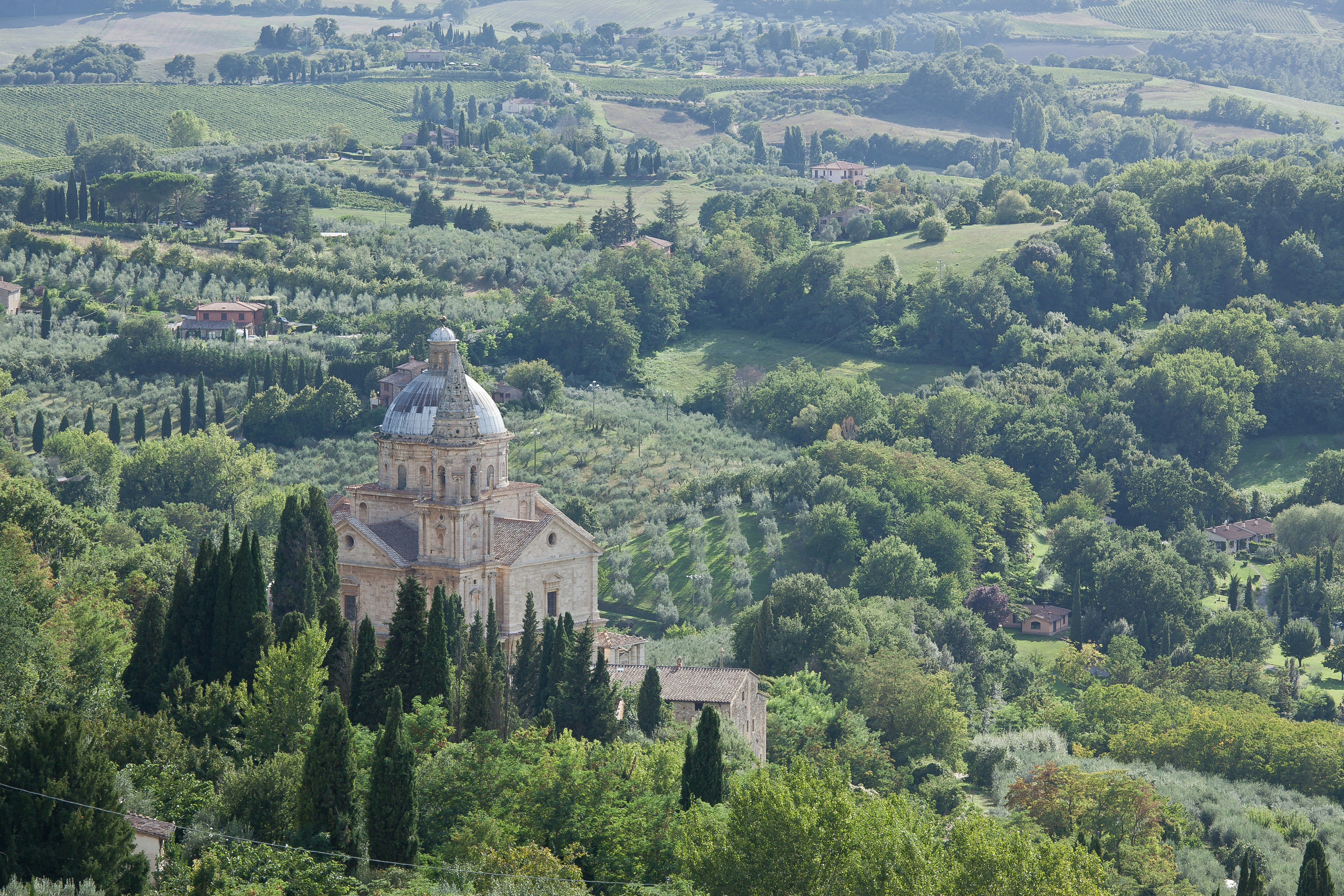 Historic church nestled in lush green hills, surrounded by olive groves and cypress trees.