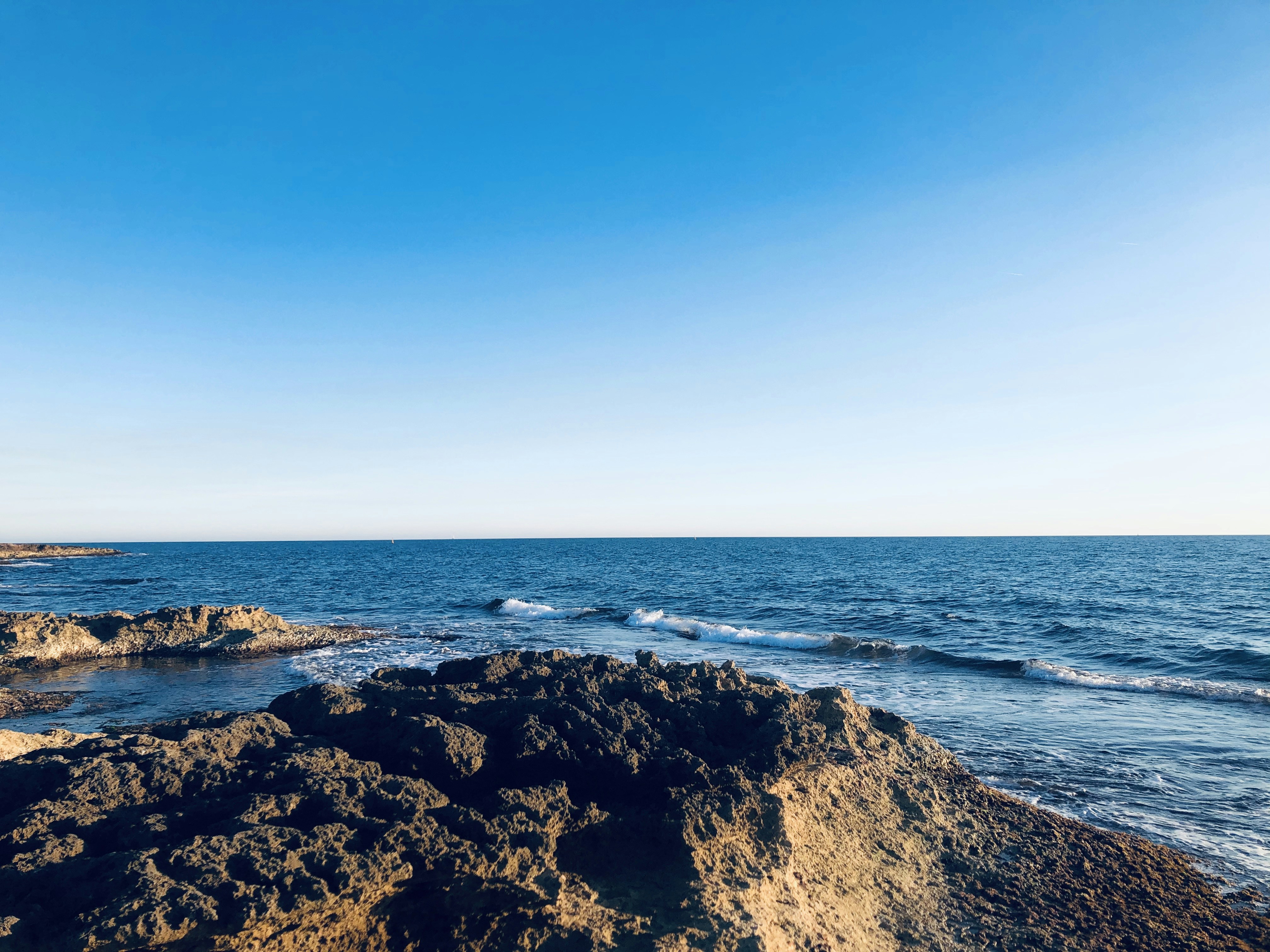 Rocky shoreline meeting a calm sea under a cloudless blue sky.