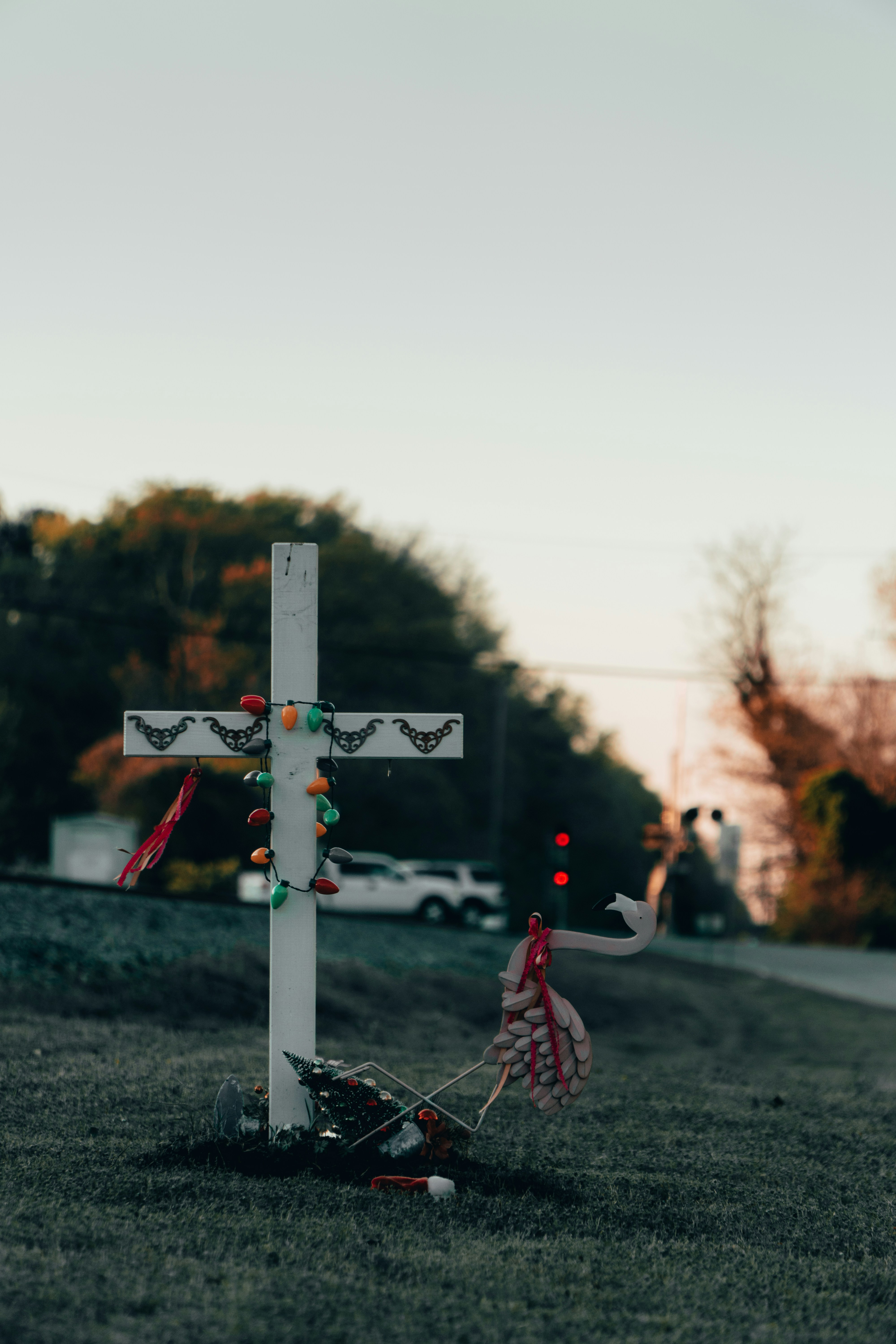 A decorated white cross stands solemnly at the roadside, adorned with colorful lights and personal mementos, symbolizing remembrance and tribute.