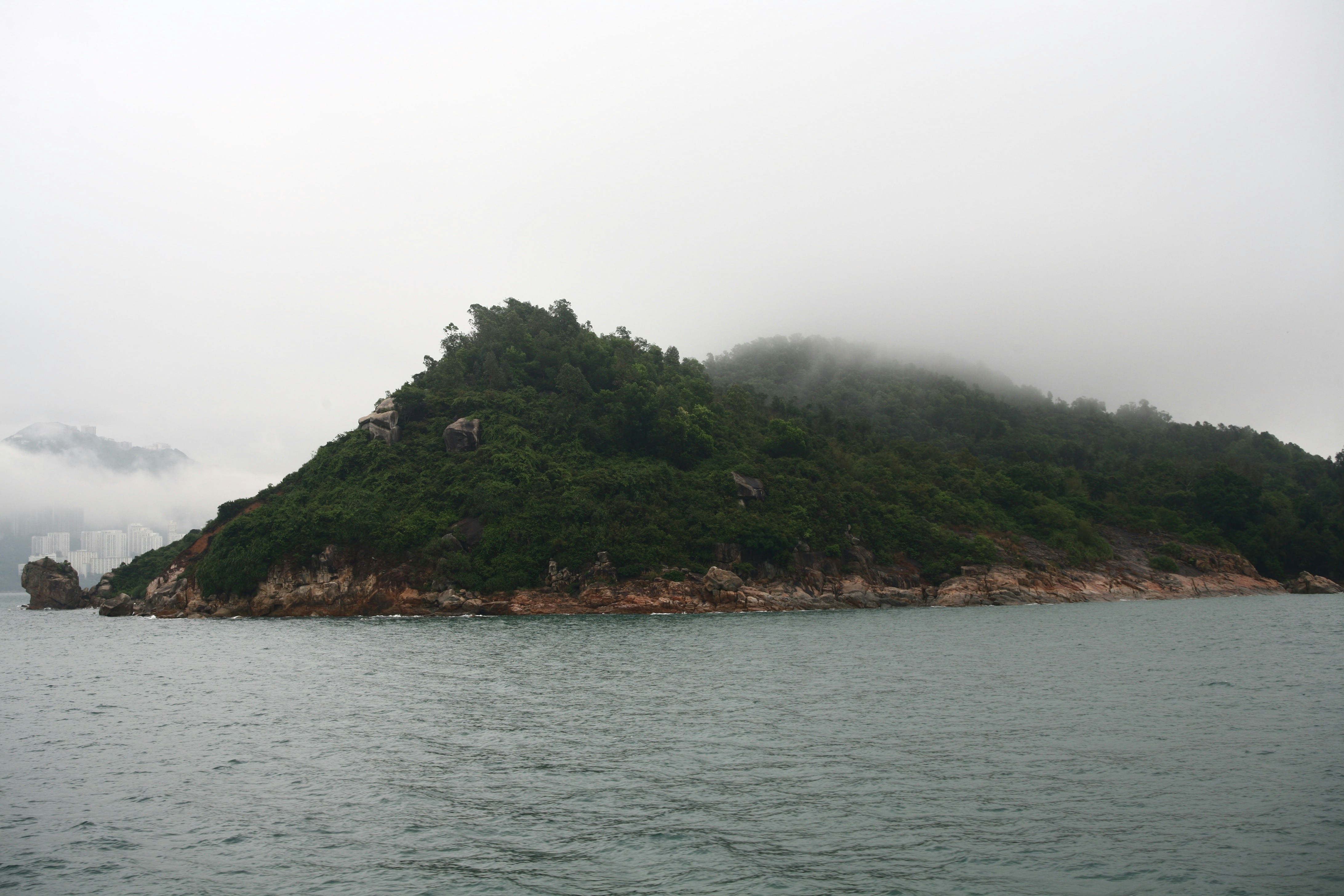 Secluded island shrouded in mist, surrounded by tranquil waters. Lush greenery contrasts with rocky shoreline.