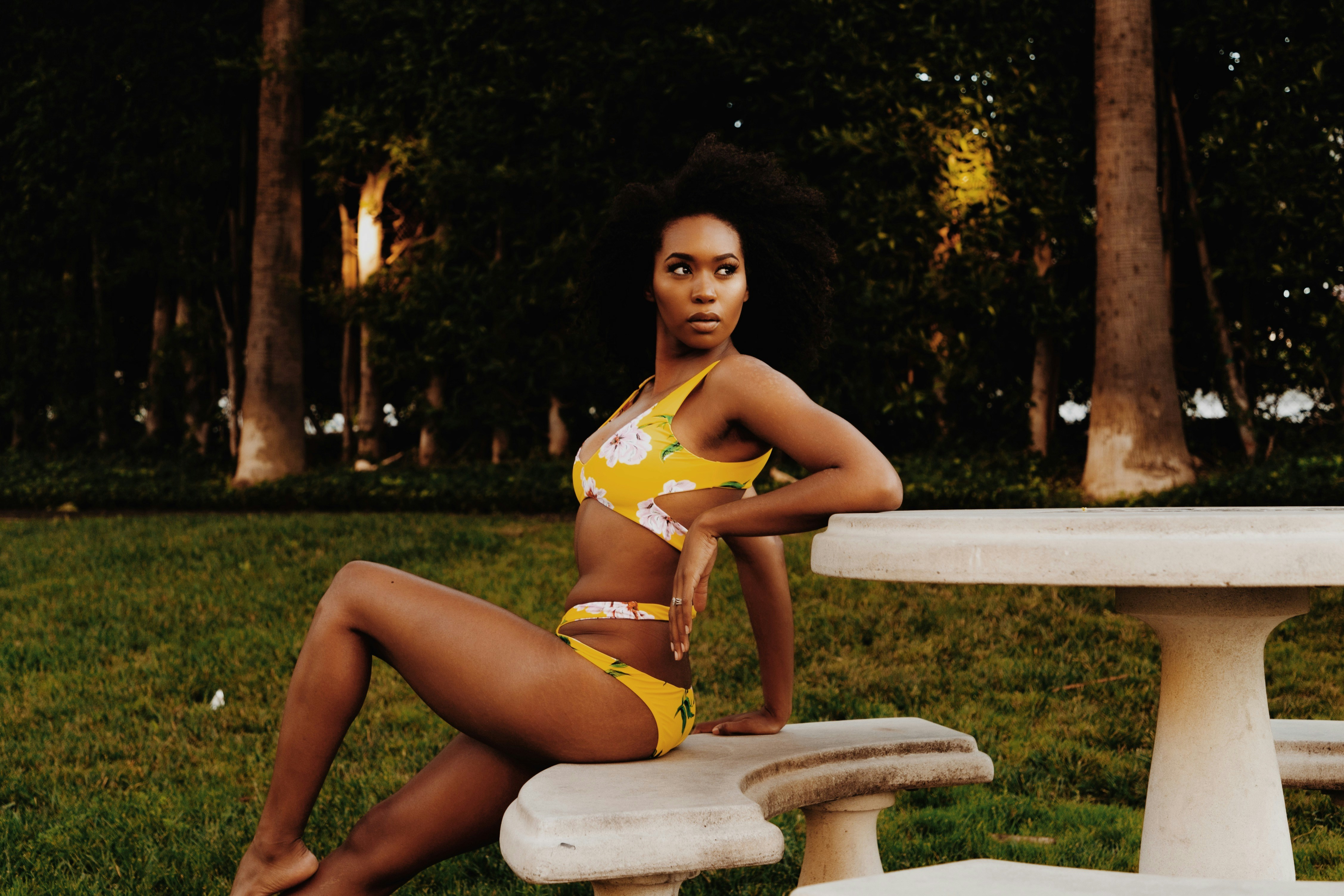 woman in yellow and red floral swimsuit sitting on white concrete bench during daytime