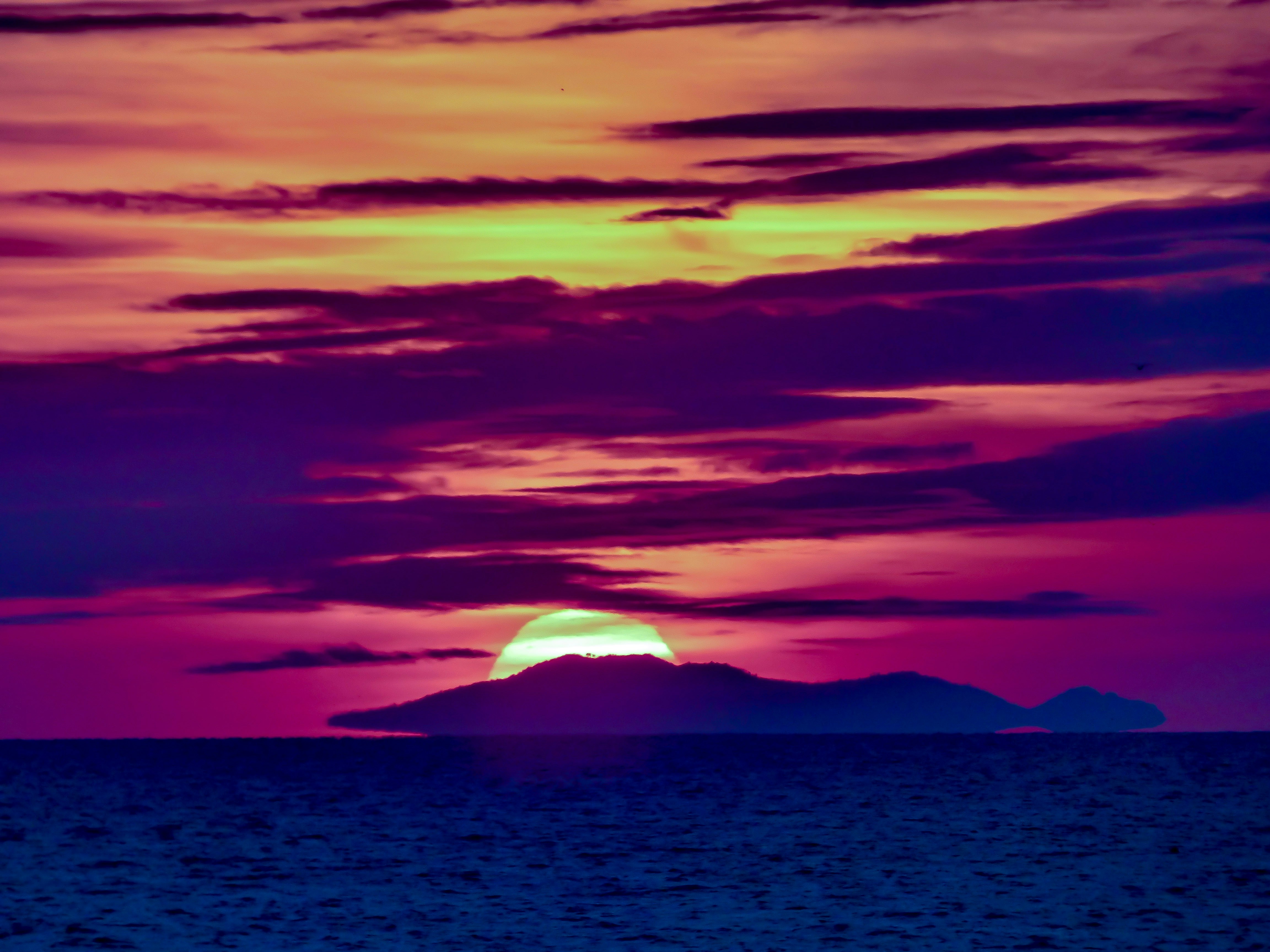 Vibrant sunset over an ocean horizon with silhouetted islands and dramatic cloud formations.
