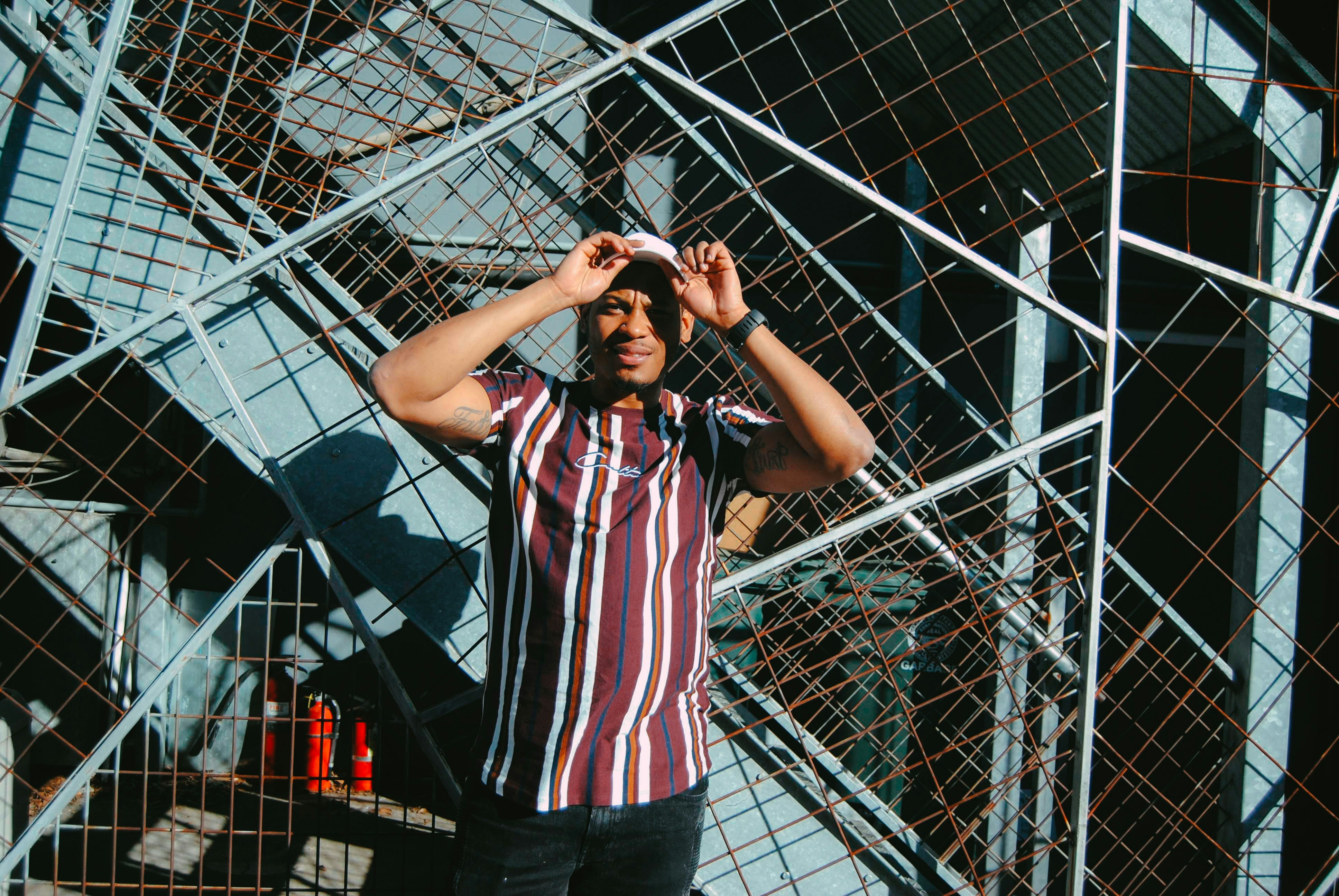 Man in a striped shirt stands against a backdrop of industrial metal structures.